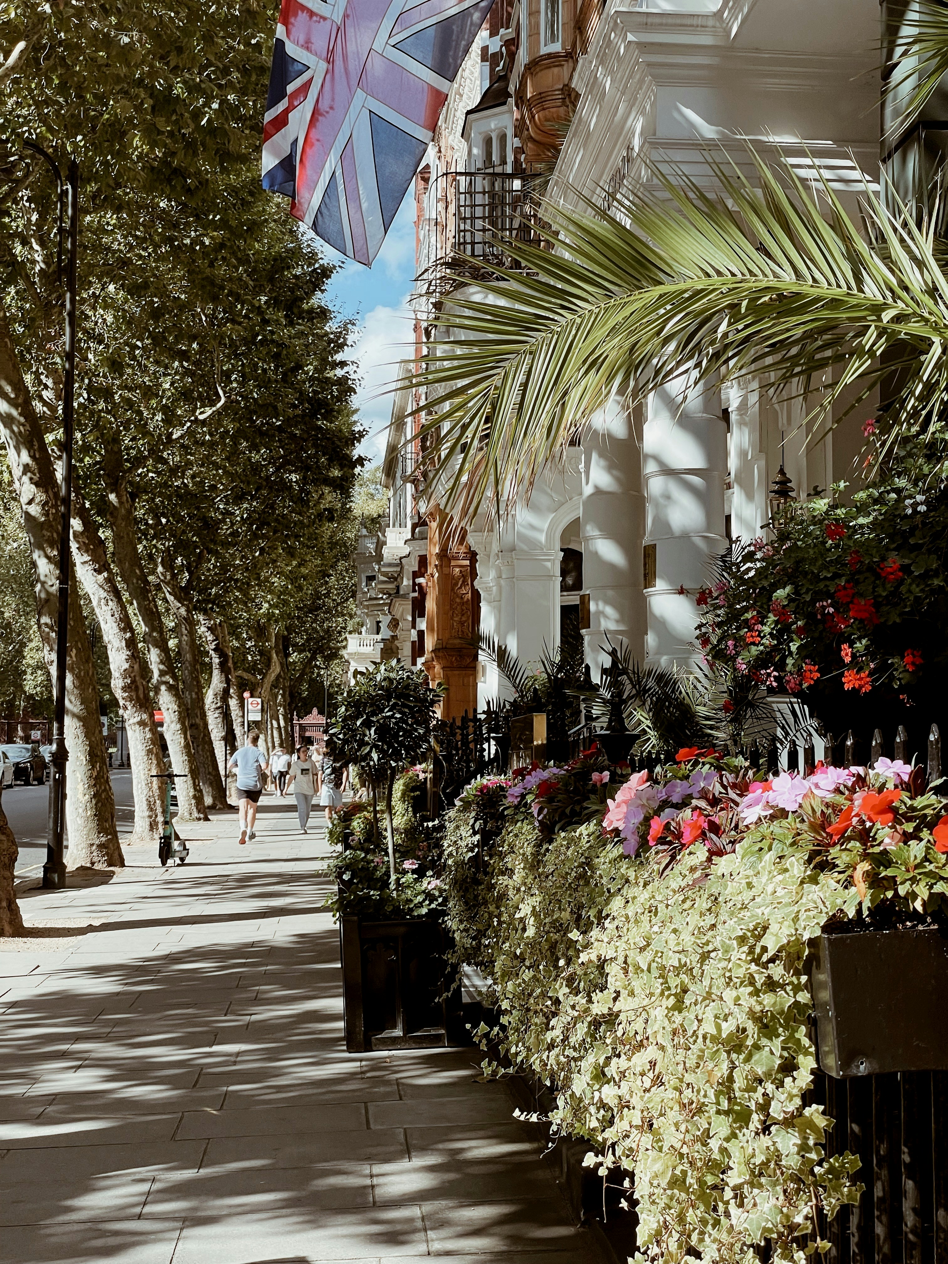 British Flags and Sunlit Terrace along a Lush City Avenue