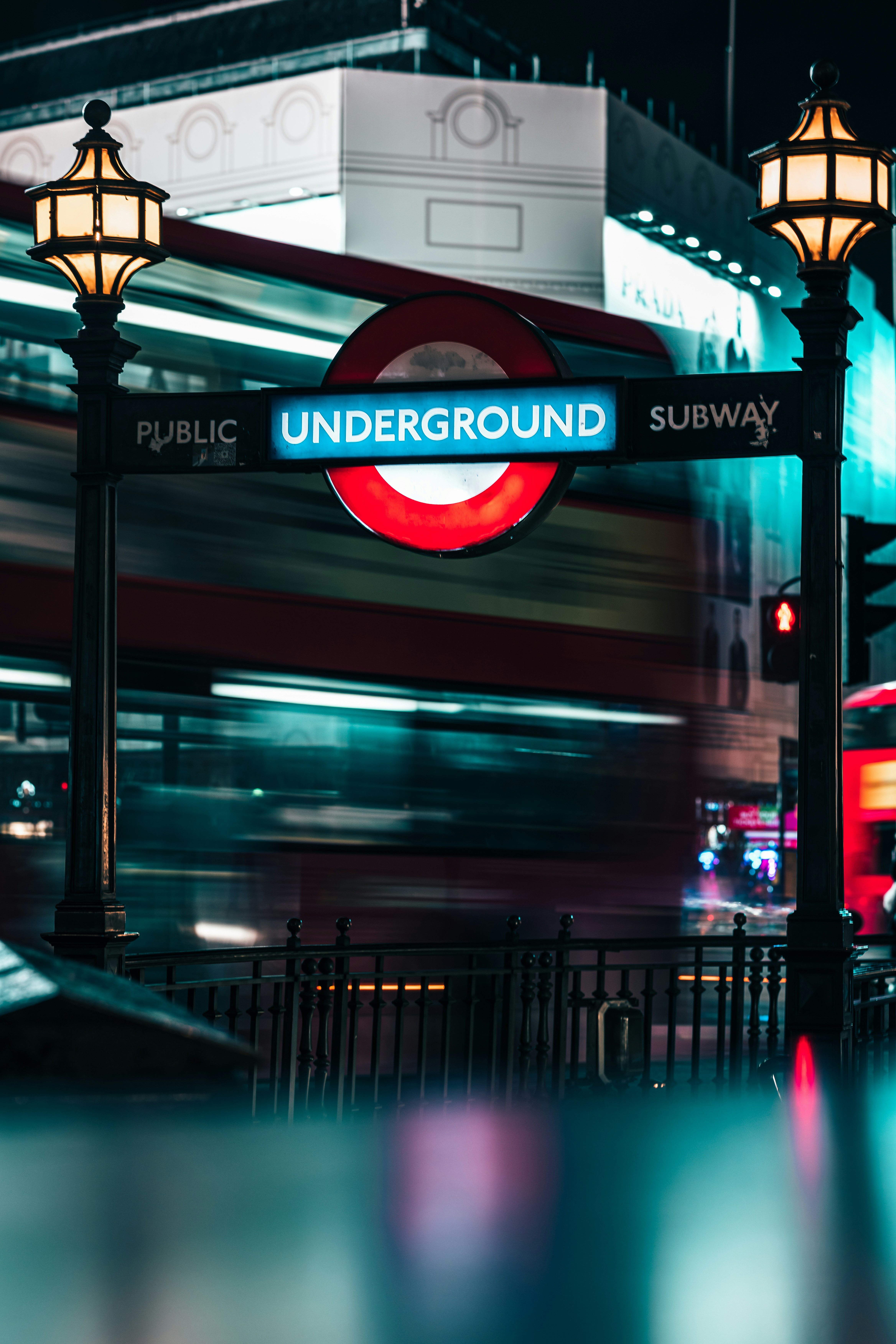 Illuminated London Underground sign amidst a blur of passing buses at night, showcasing the city's vibrant transit life.