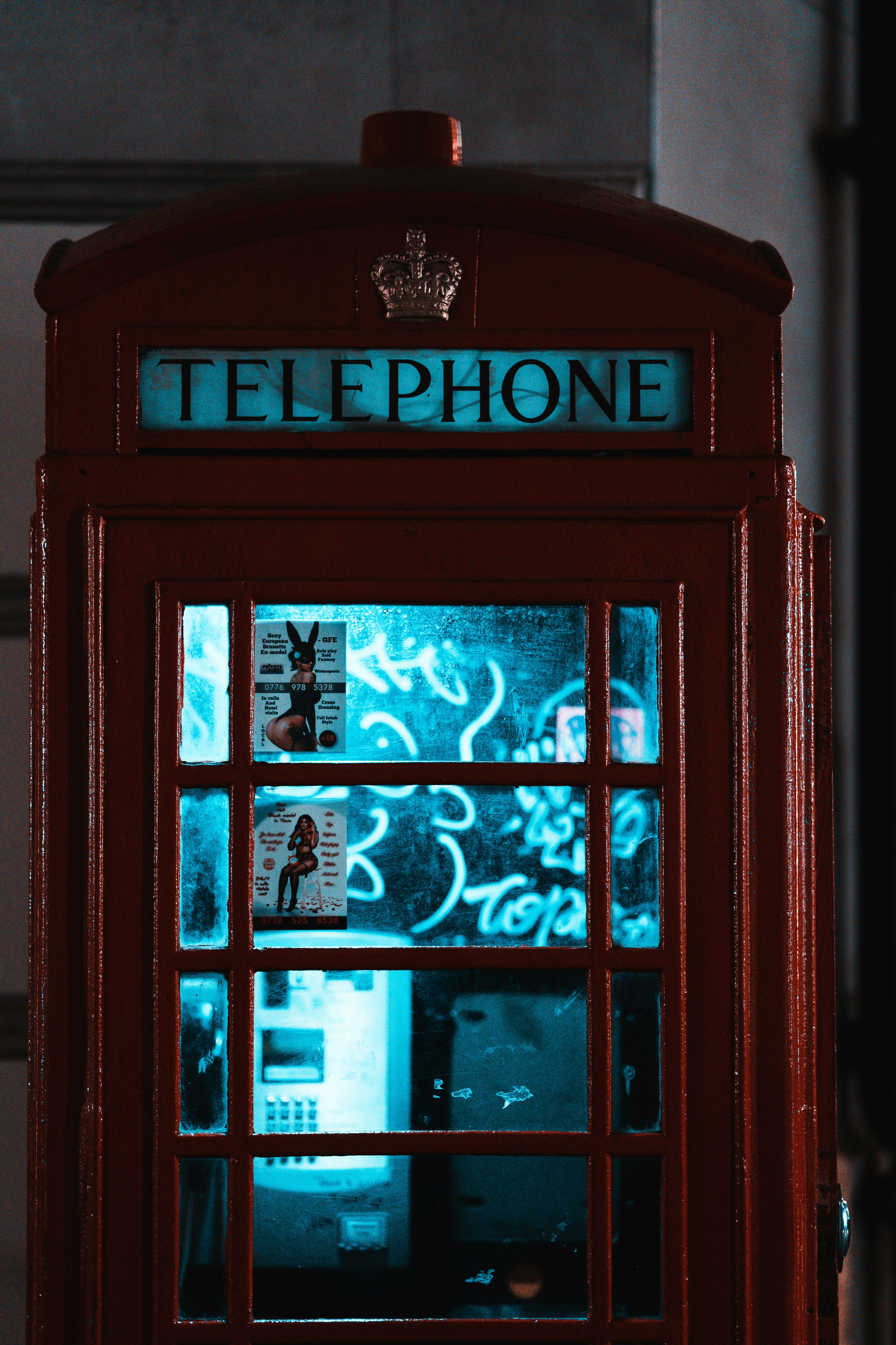 Crimson Phone Booth Illuminated by Electric Blue Neon Graffiti