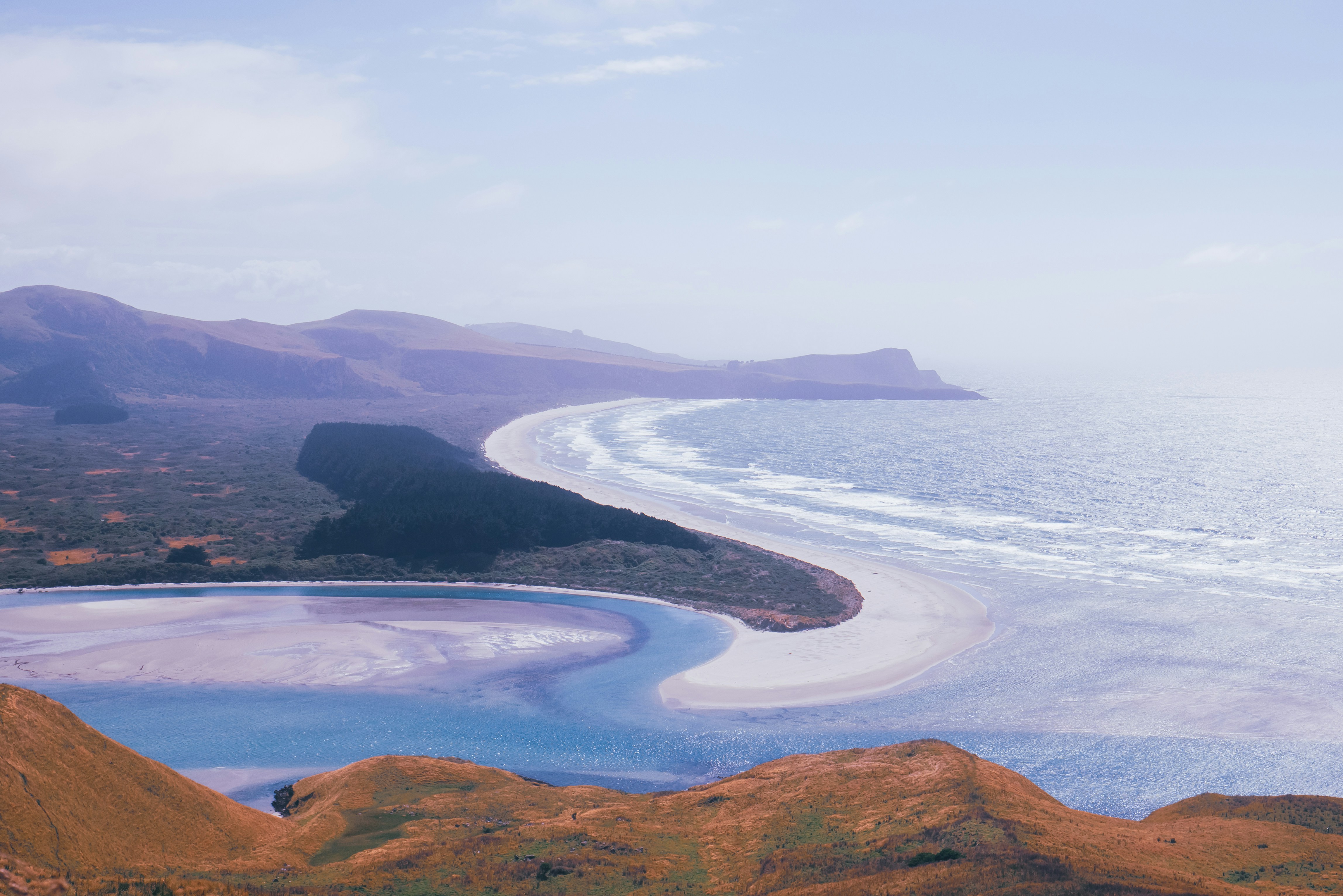 Sweeping beach curves alongside rugged hills under a clear sky.