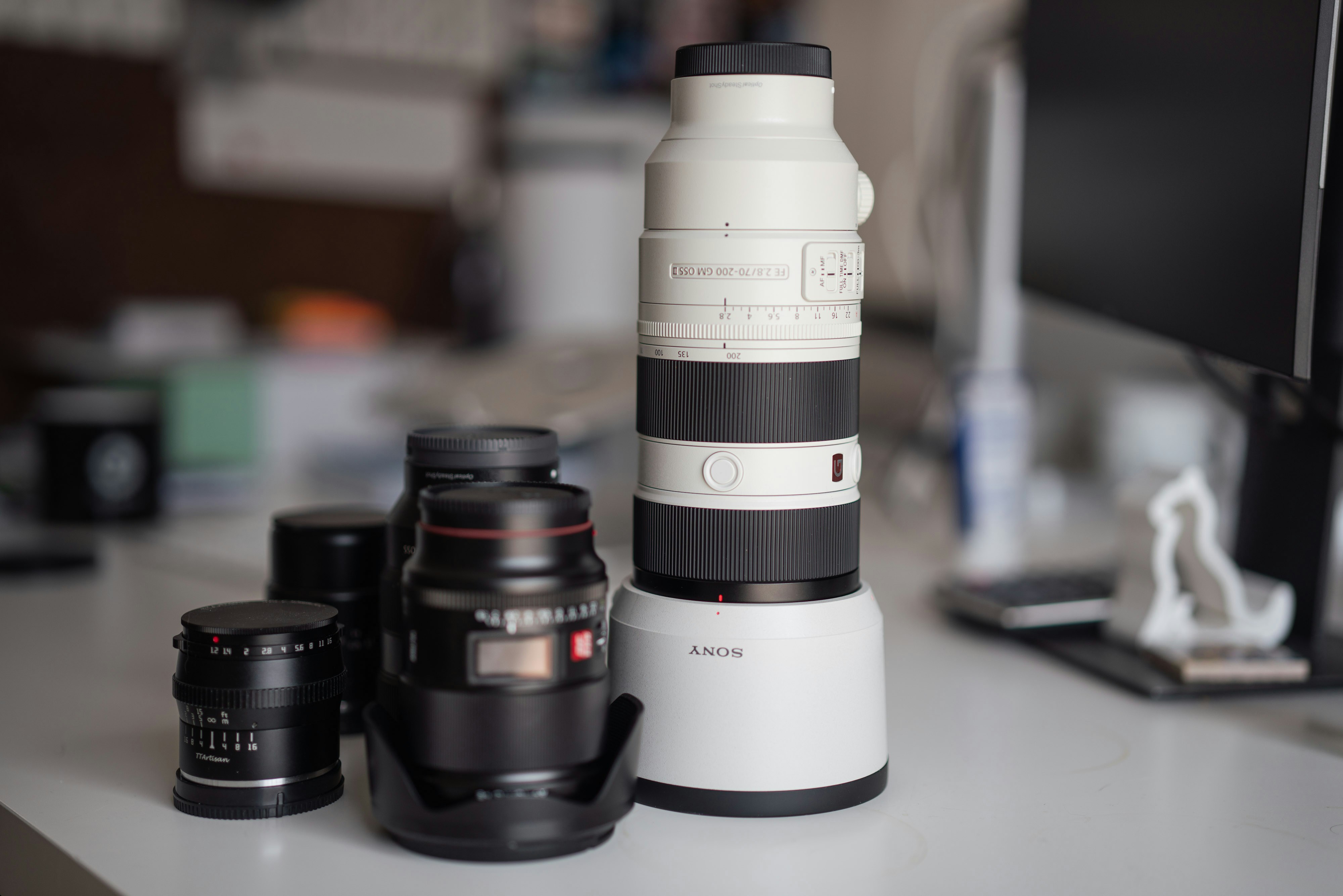 White telephoto with black accents stands tall among a trio of lenses on a studio desk