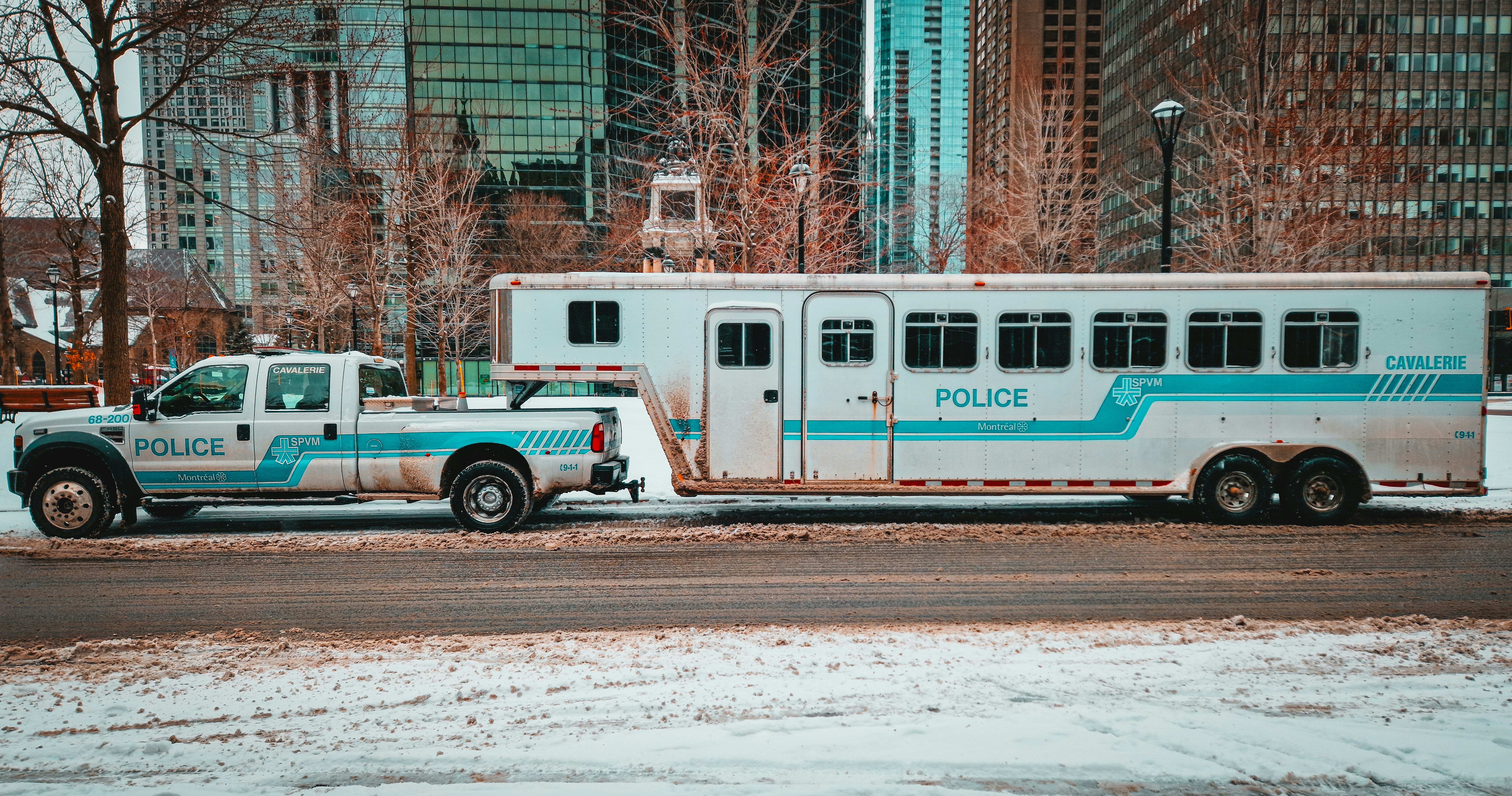 Snowbound City Convoy: A Long Police Transport Trundles Past a Glassy Skyline