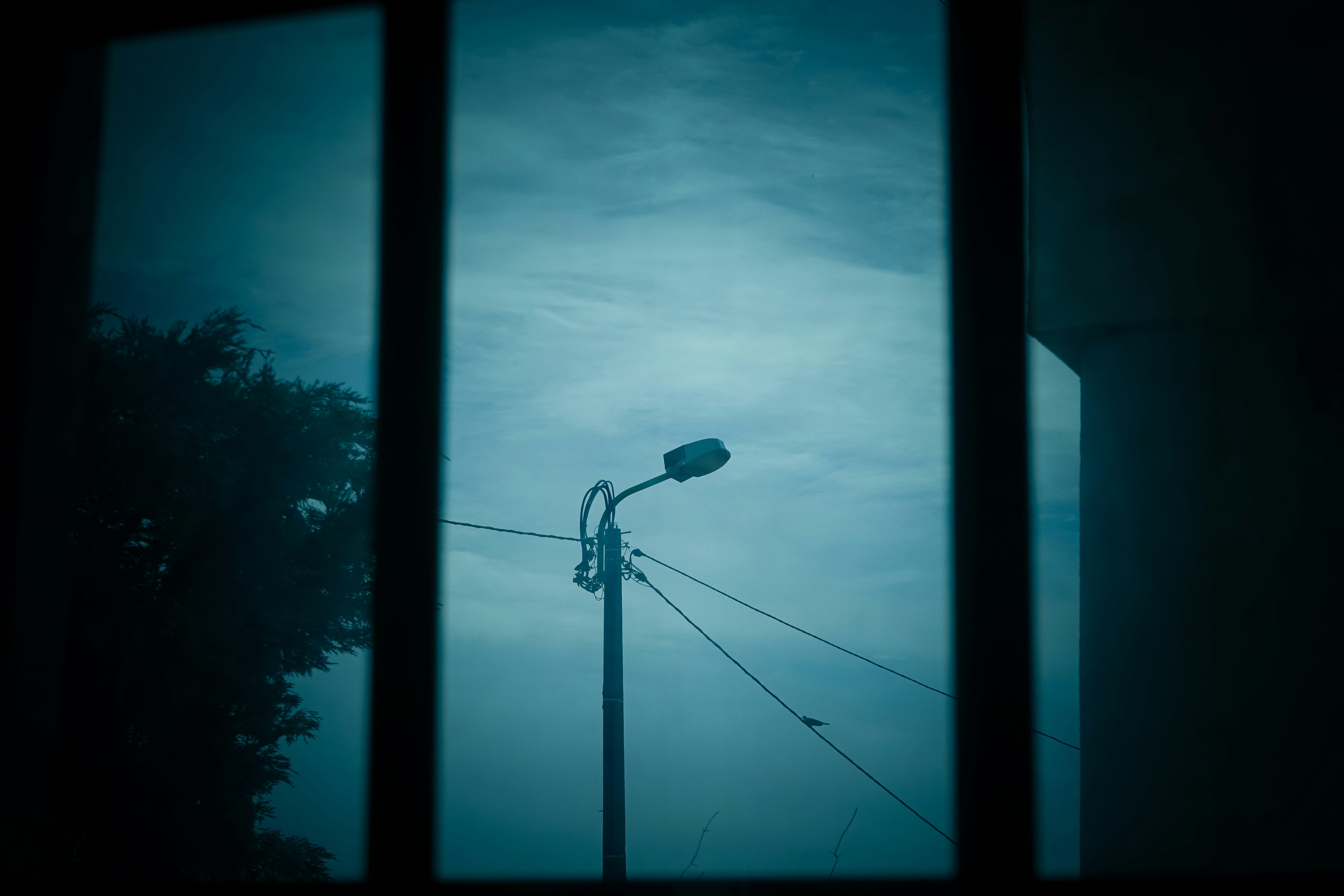 Between Bars and Sky: A Dim Streetlamp through a Window