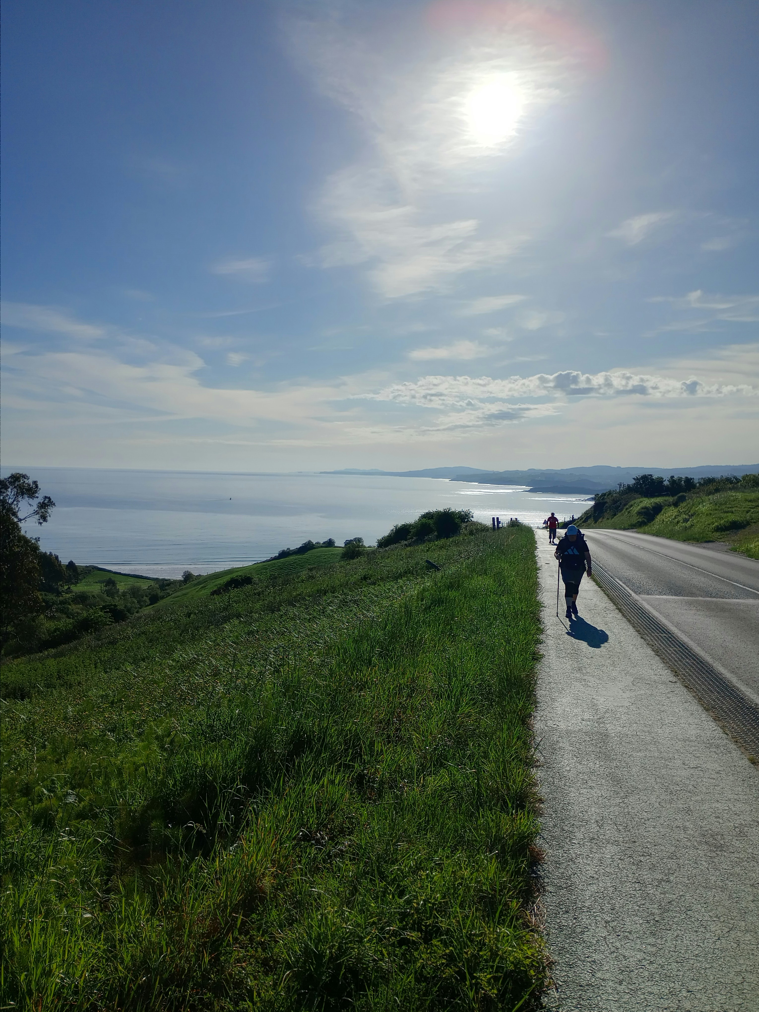 Lone cyclist on a sunlit coastal road heading toward the horizon