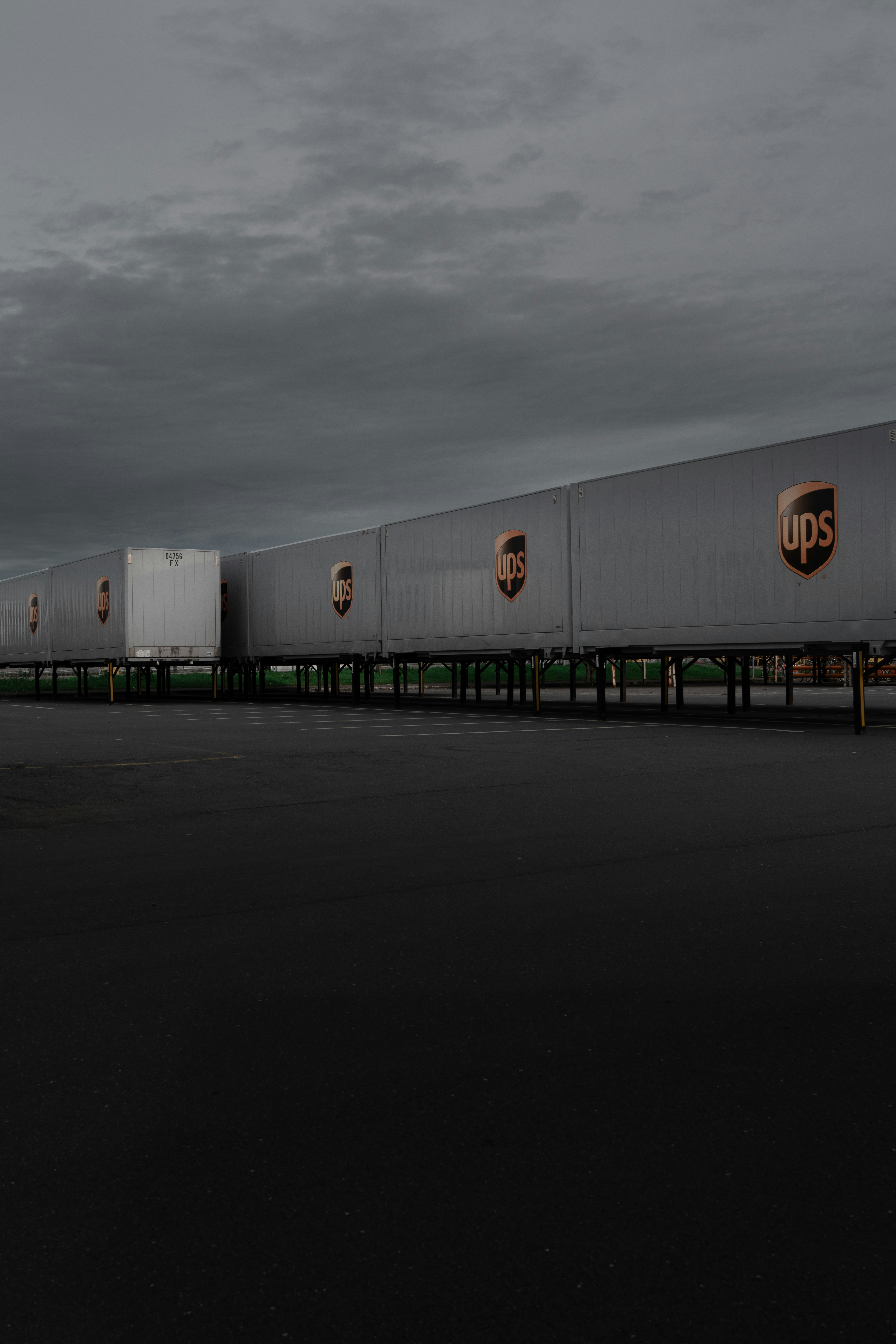 A row of UPS trailers parked under a moody sky, showcasing the logistics hub's organized layout. The scene captures the essence of transportation efficiency.