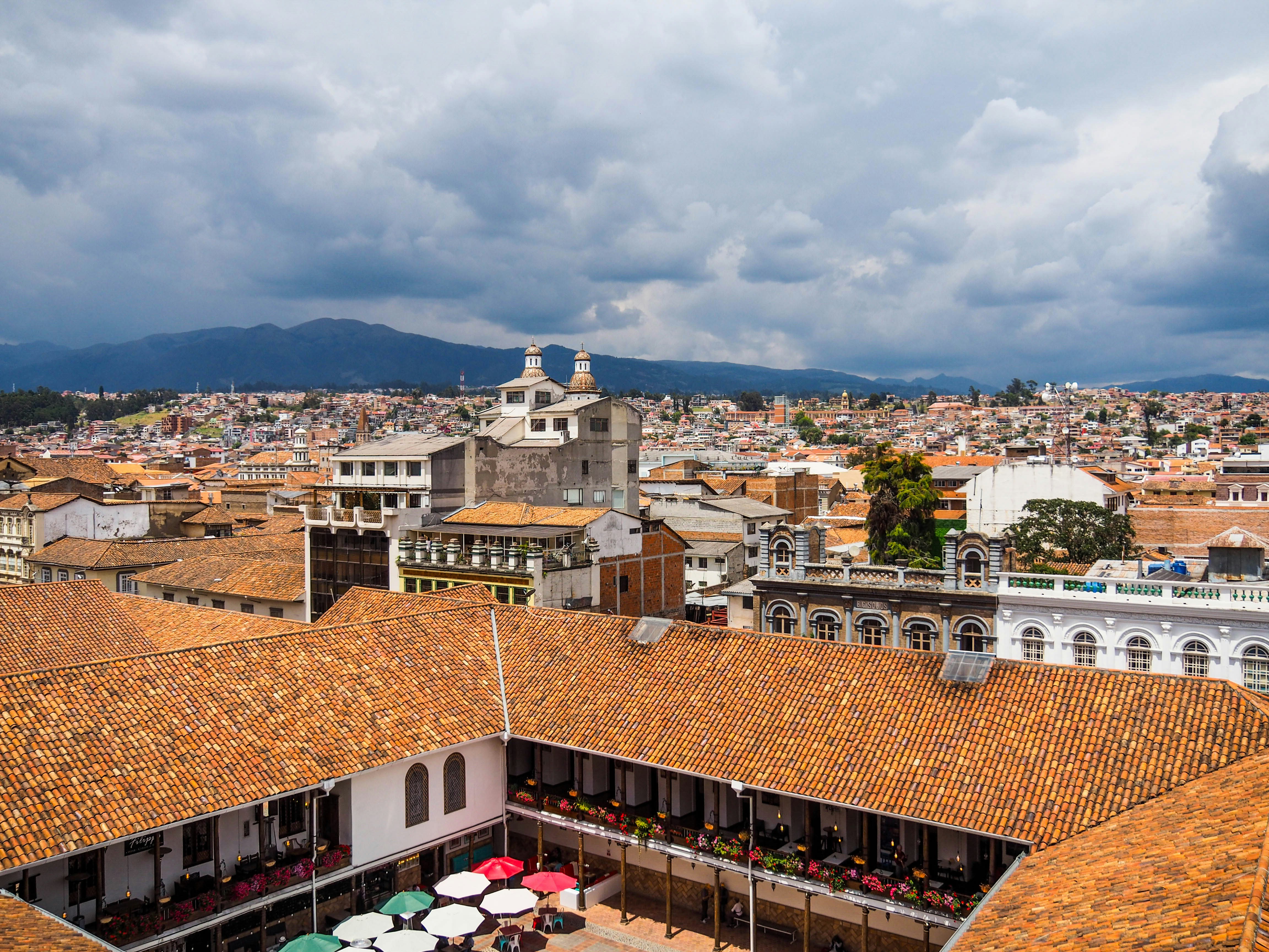 Panoramic view of a cityscape with terracotta rooftops and a cloudy sky.