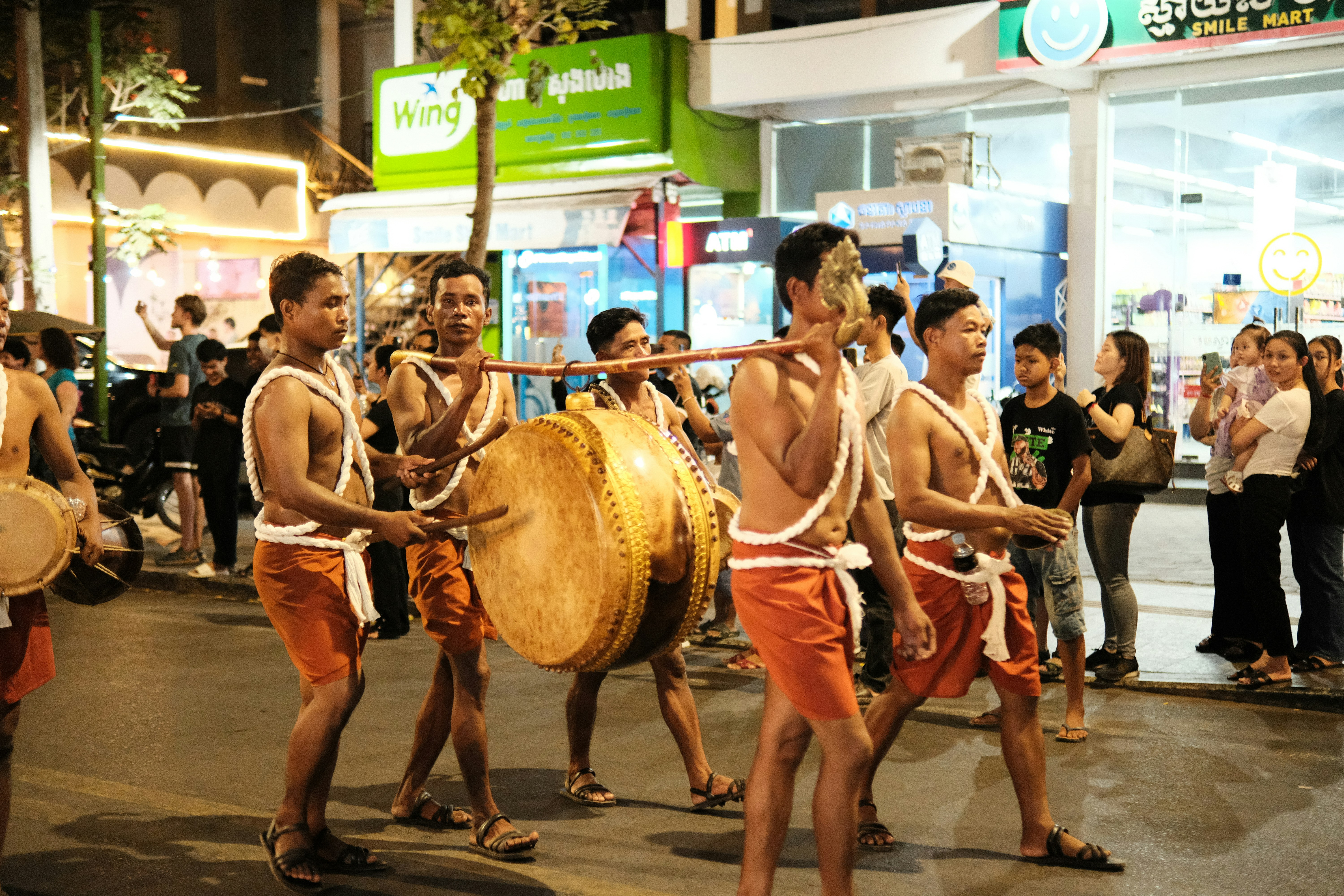 Traditional drummers in ceremonial attire performing in a lively street parade at night.