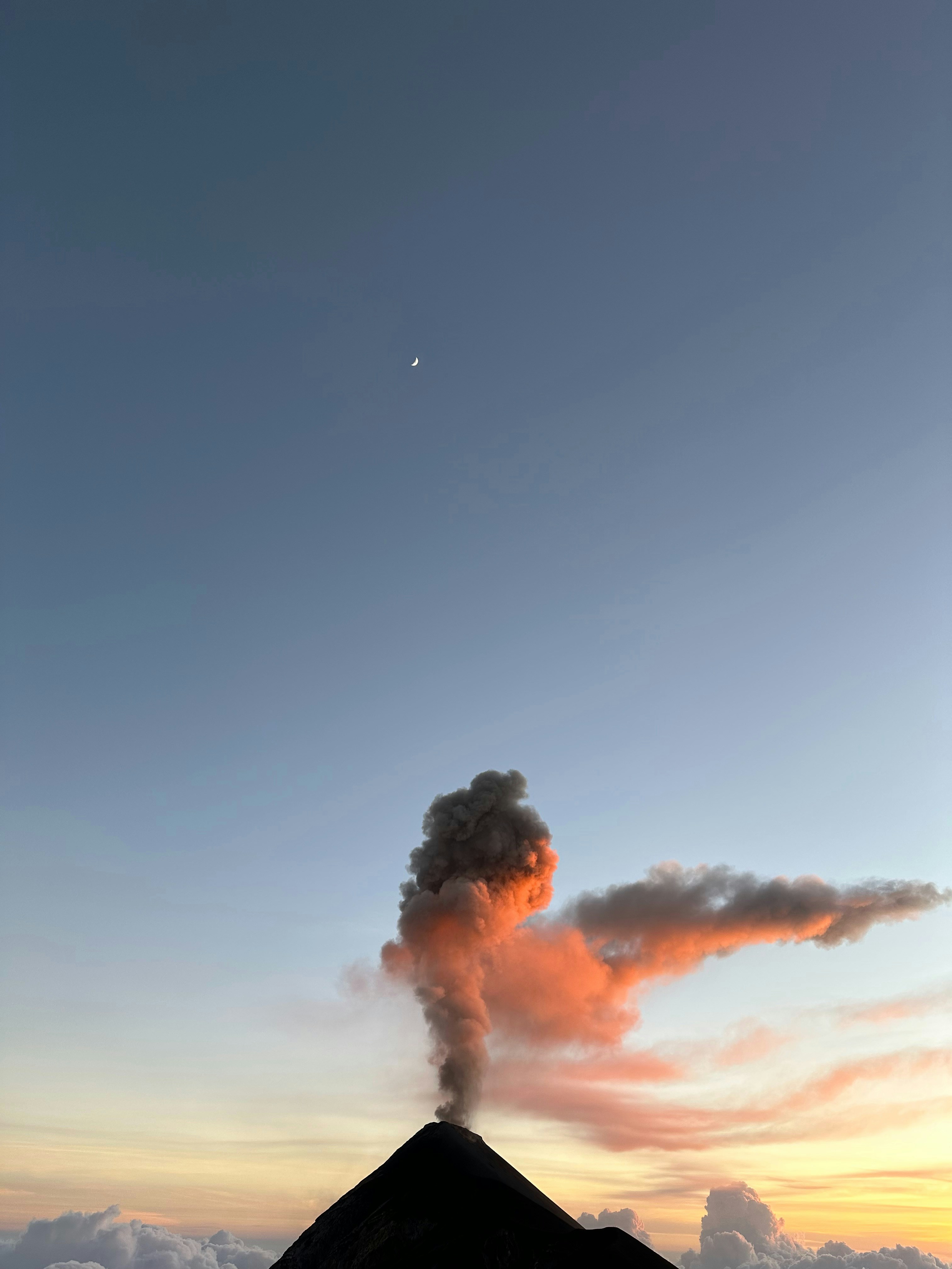 Volcano emits a plume of smoke under a twilight sky with a bright star overhead.
