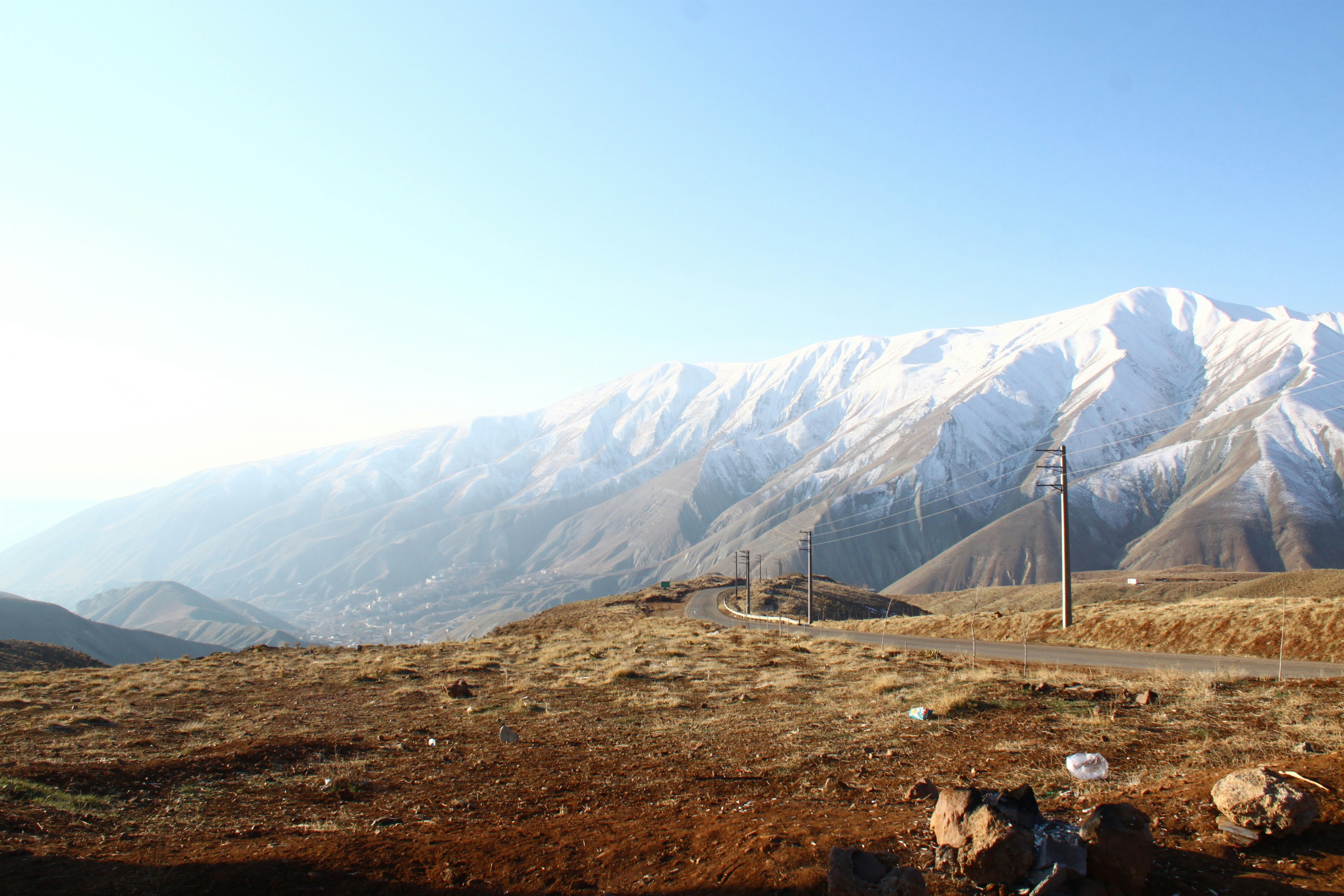 Snow-covered mountains rise majestically above a winding road, showcasing the tranquility of nature in a remote landscape.