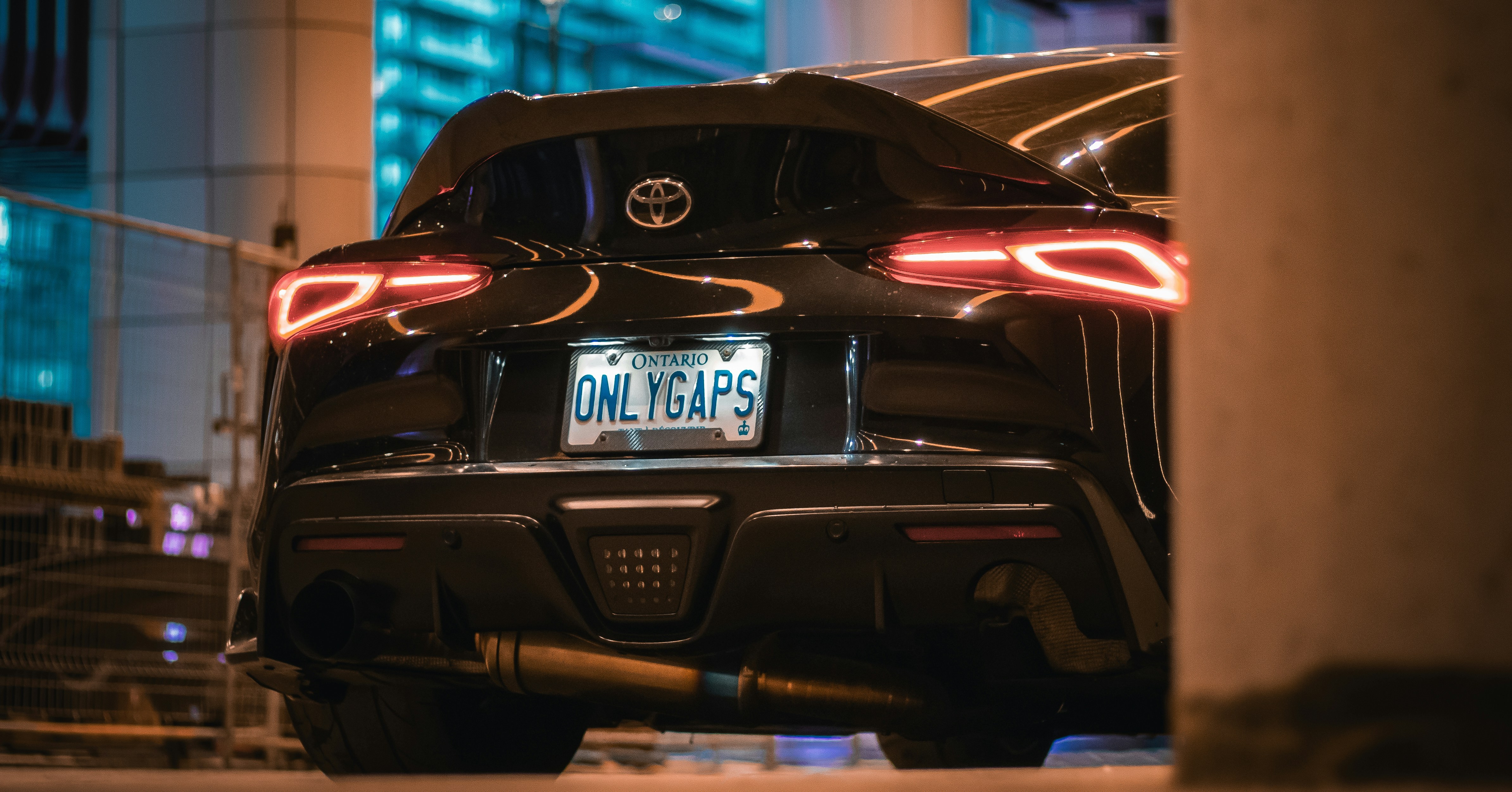 Sleek black sports car parked in a modern urban setting, showcasing its distinctive rear design and illuminated taillights.