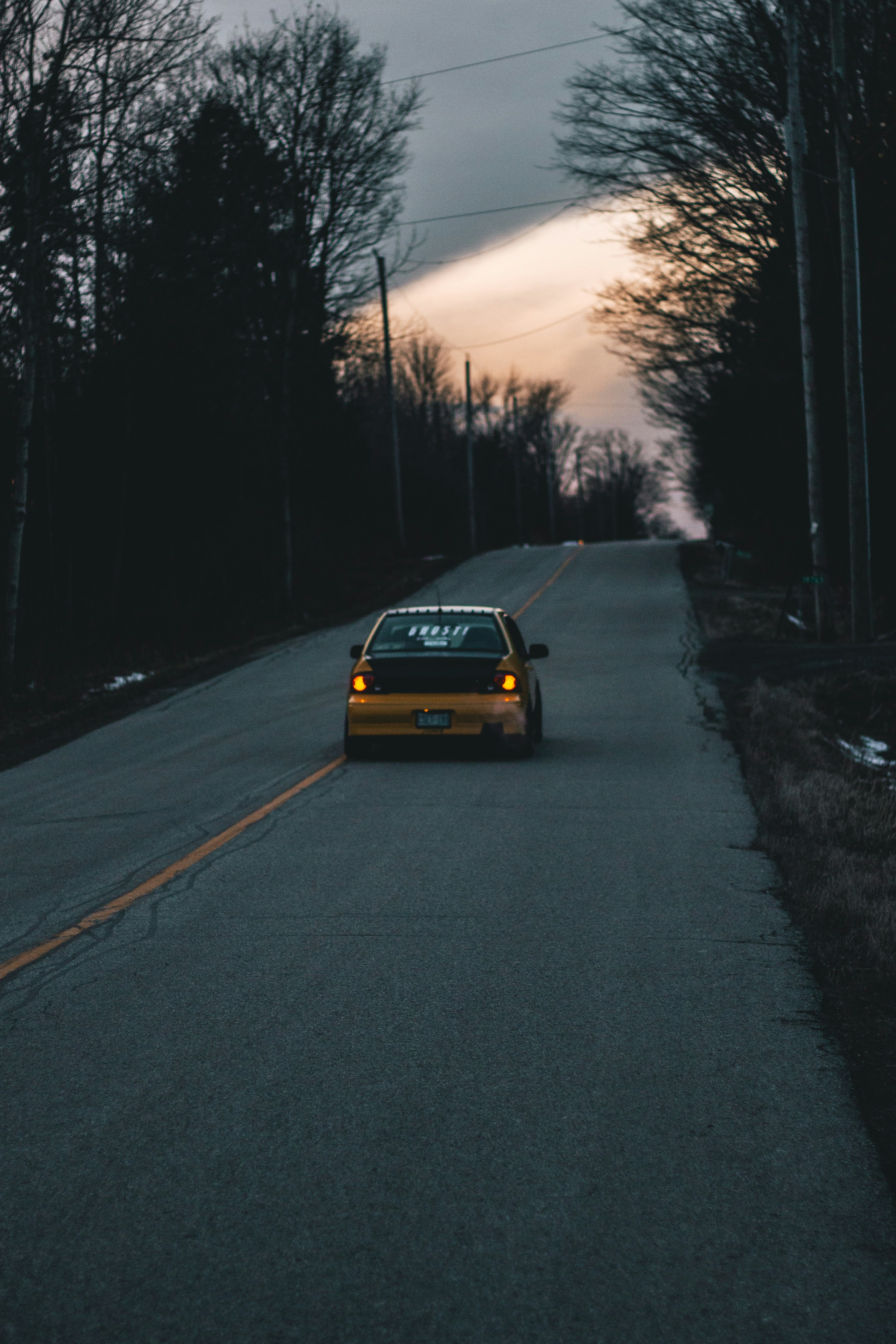 A yellow car driving down a road next to a forest photo – Free ...