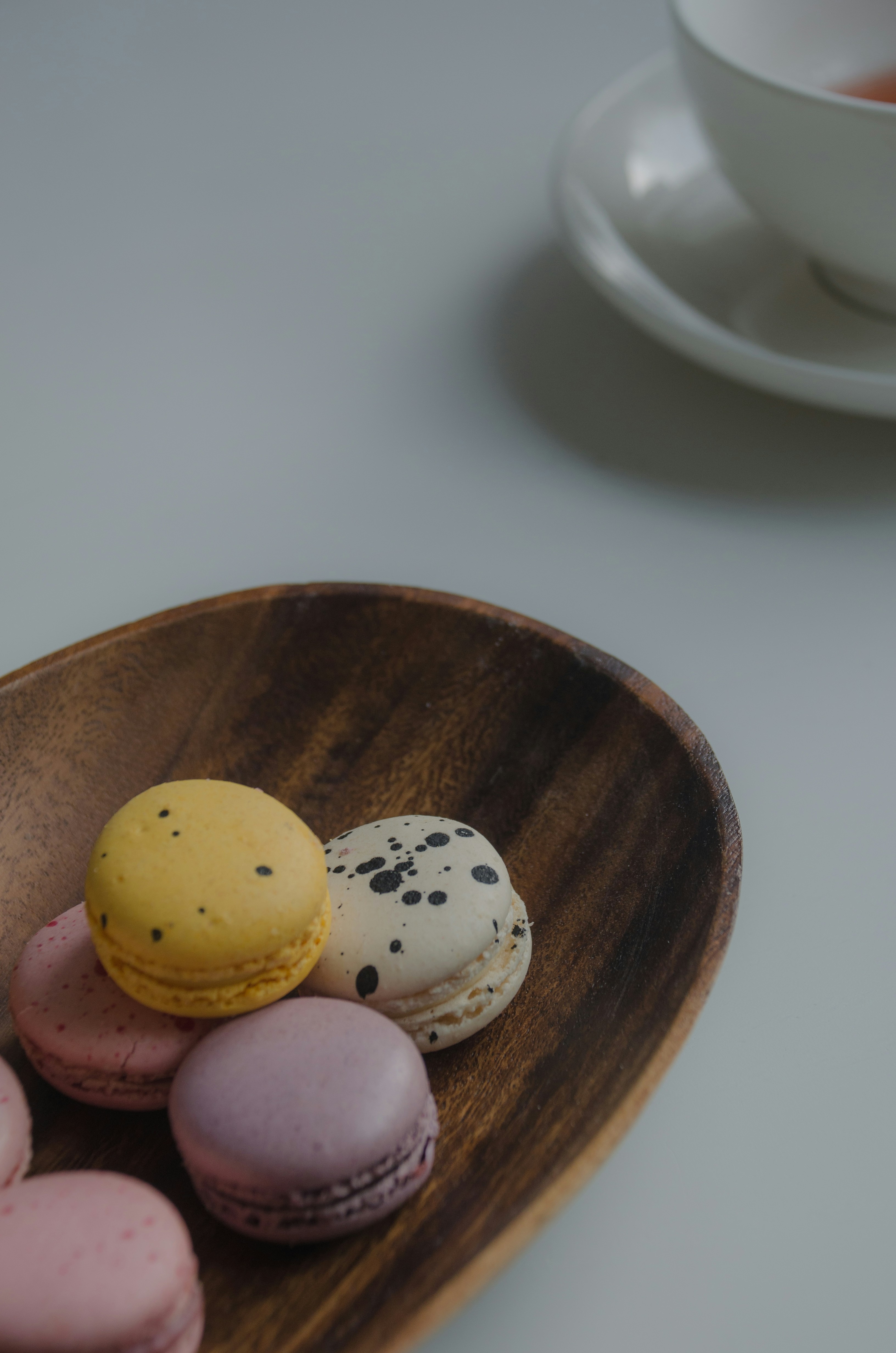 Pastel Macaron Ensemble on a Wooden Plate with a Quiet Teacup Backdrop