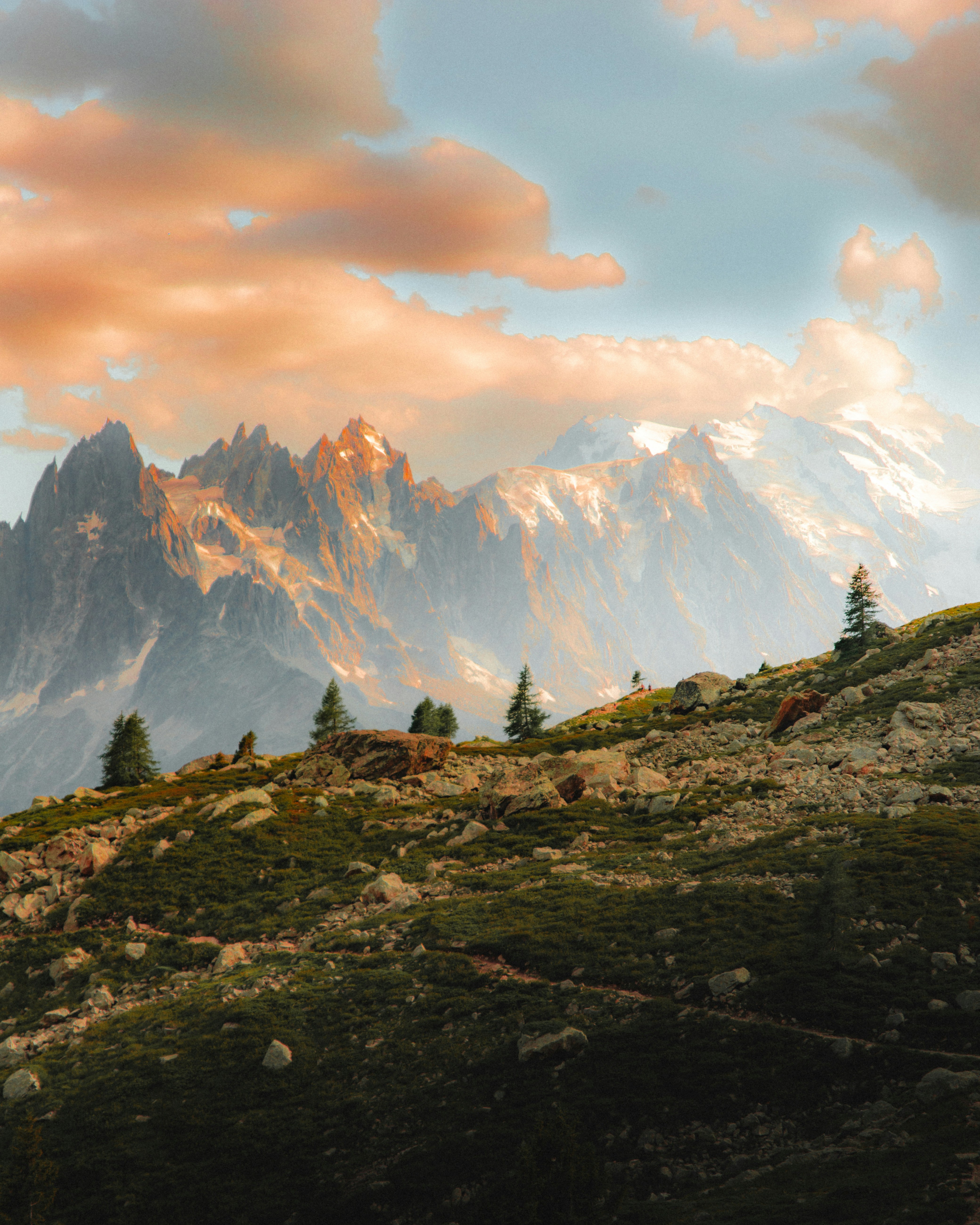Sunlit mountain range with rugged peaks under a soft, cloud-streaked sky.