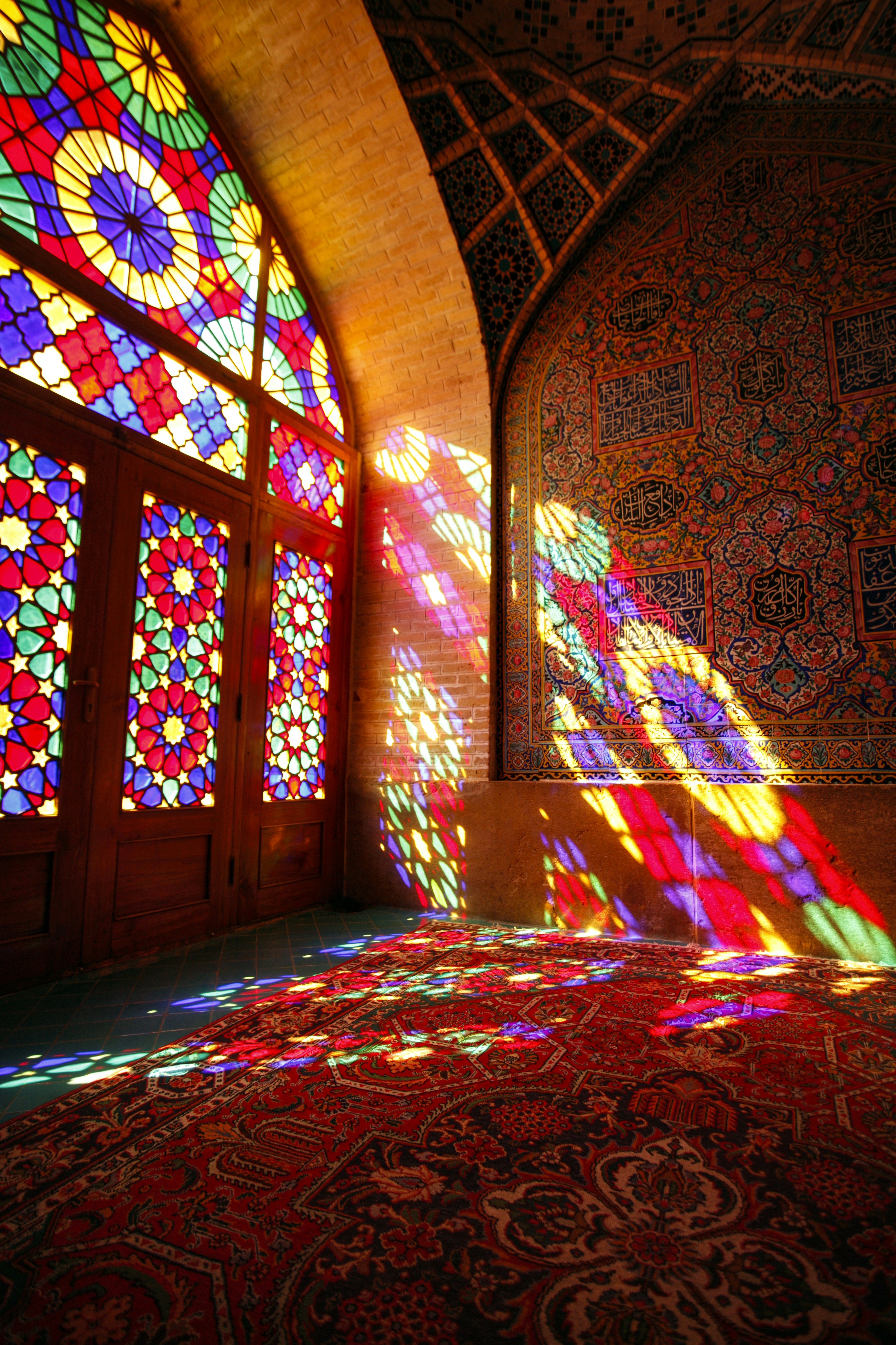 Vibrant stained glass windows casting colorful reflections on an intricately patterned carpet and wall in a historical setting.