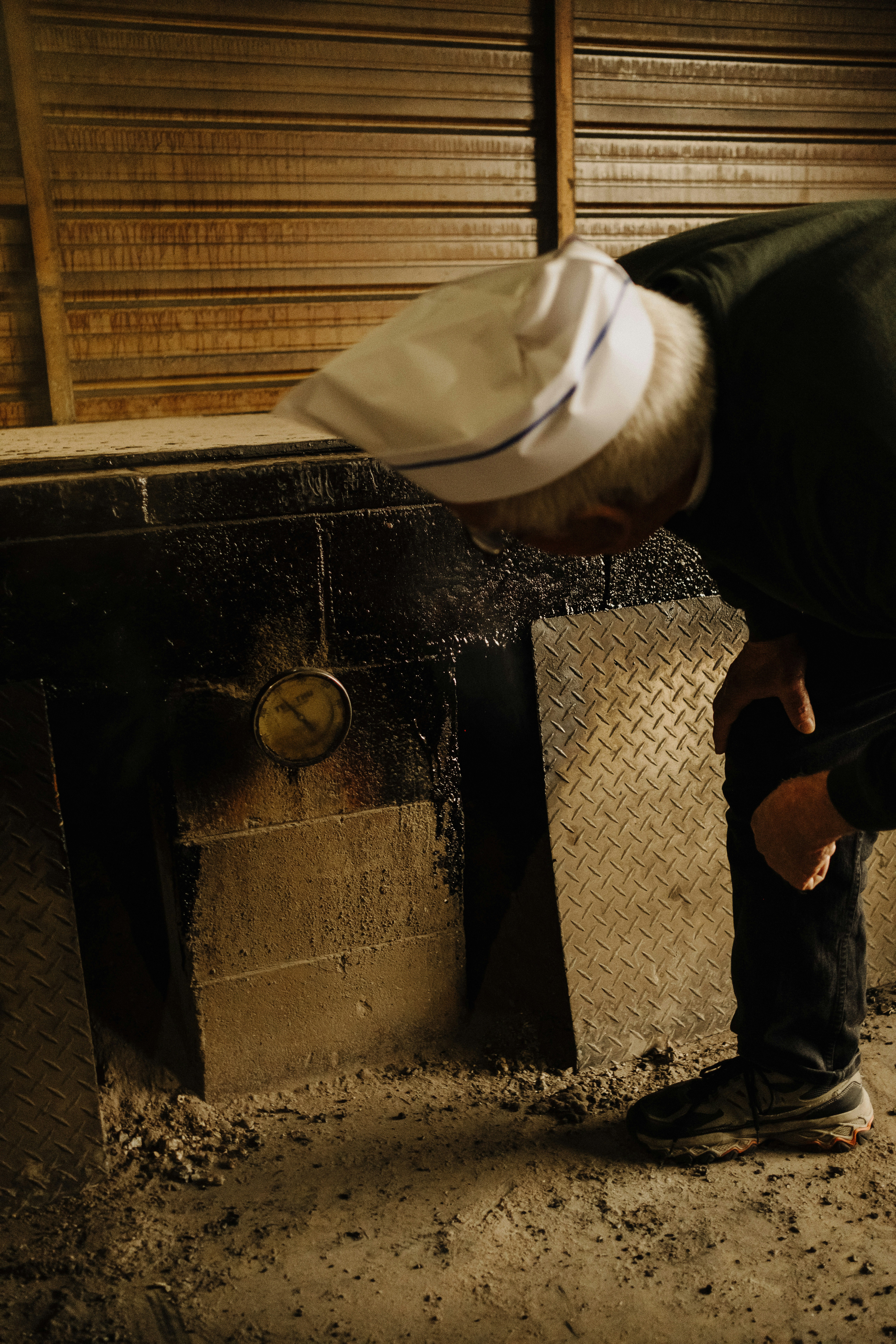 A focused individual inspects a temperature gauge on a charcoal grill in a rustic setting. The scene captures the essence of traditional craftsmanship.
