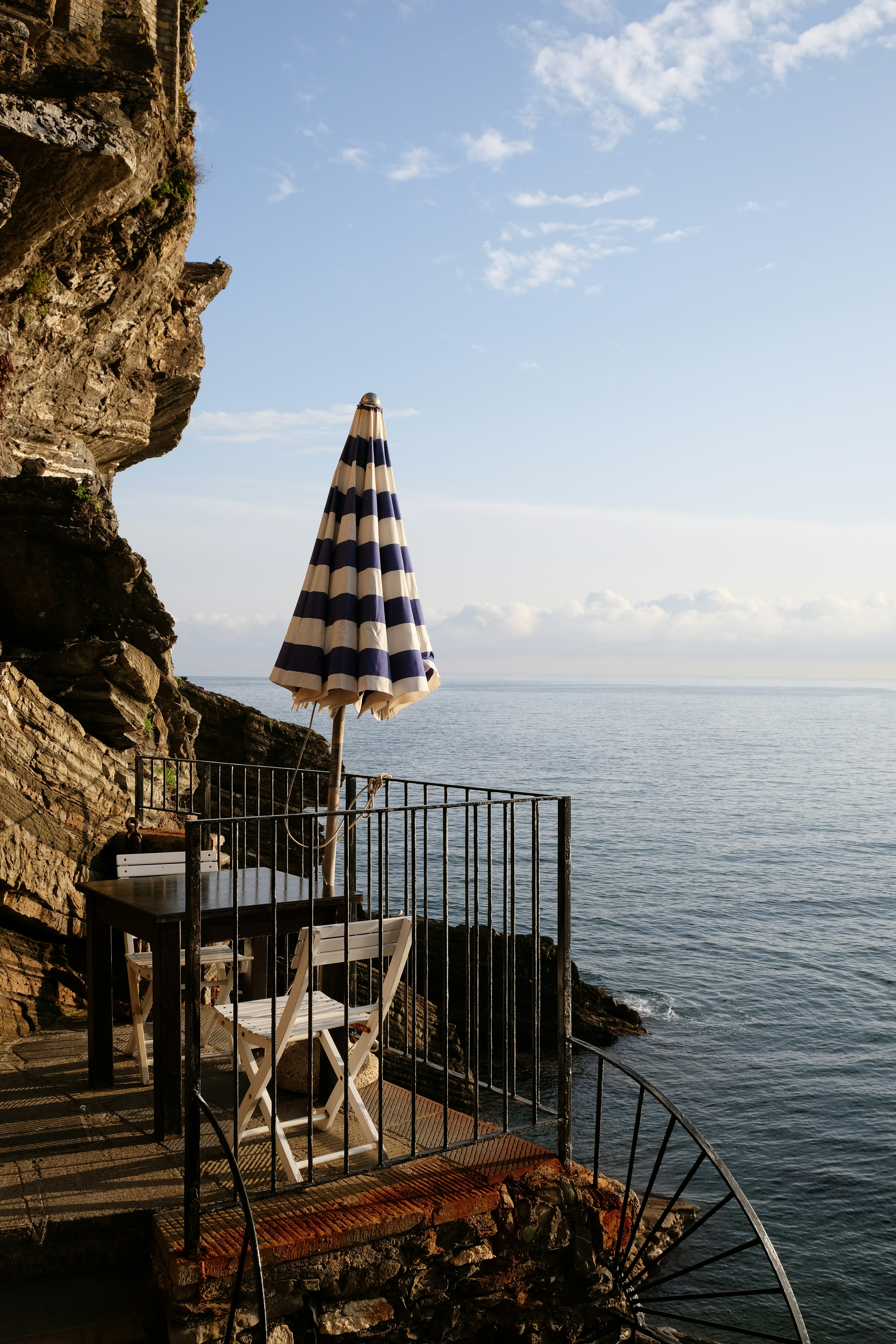 Cliffside Terrace: Striped Umbrella Overlooking a Serene Sea