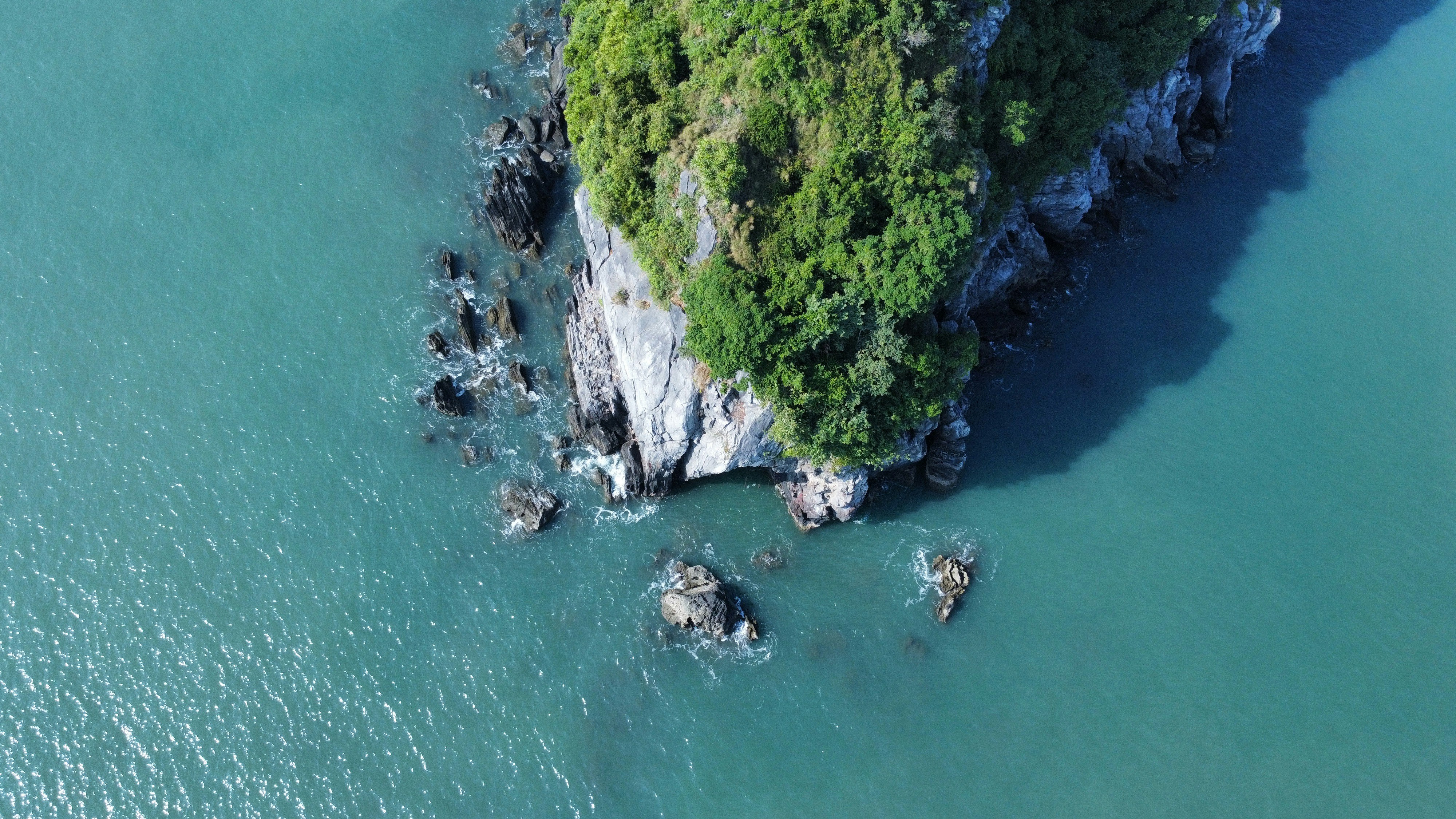 Aerial view of a lush cliff protruding into vibrant turquoise waters, surrounded by scattered rocks.