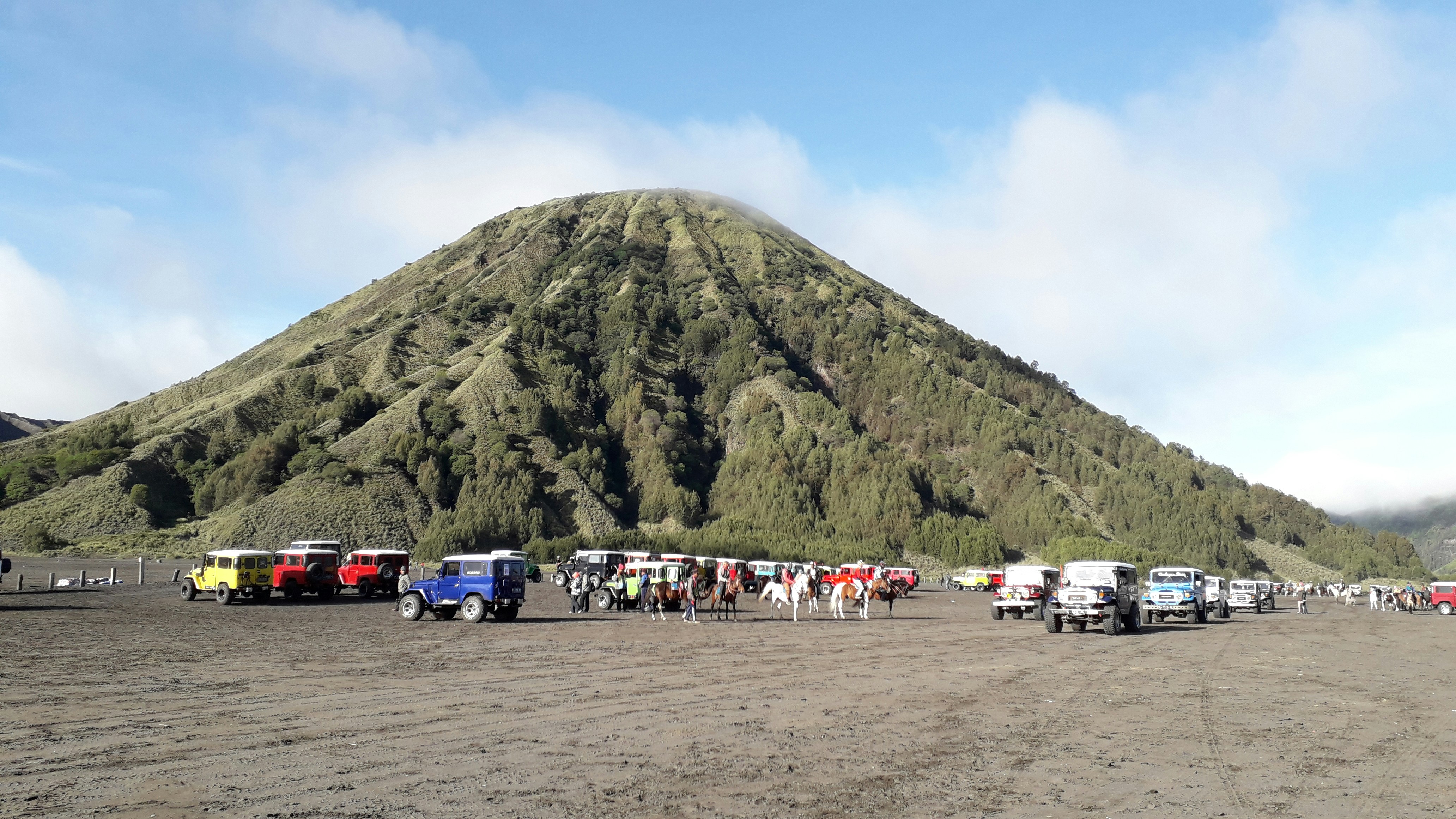 Colorful trucks lined up on a vast plain with a lush green mountain in the background under a blue sky.