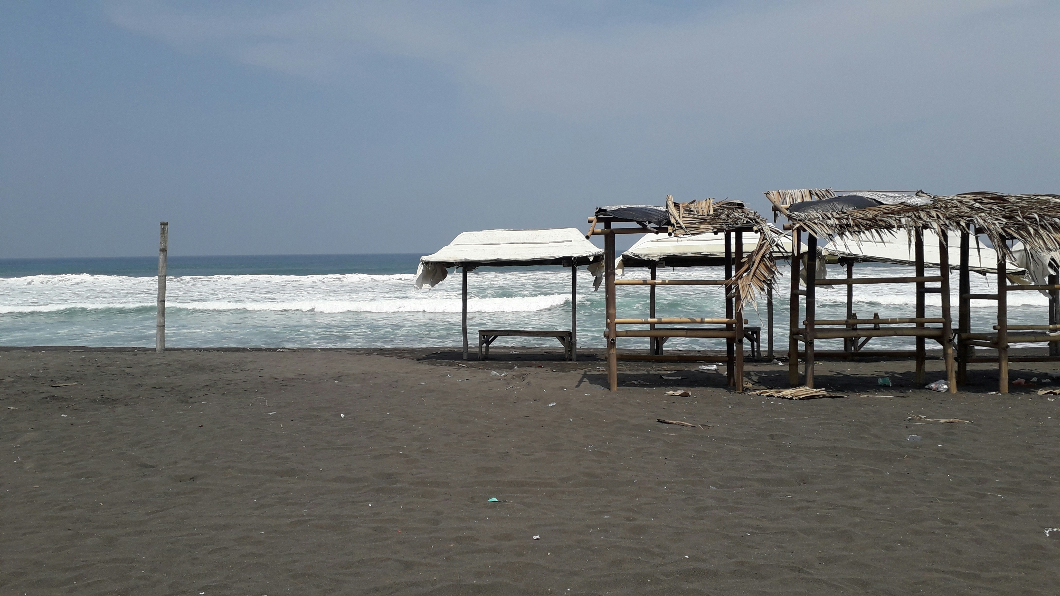 Simple wooden frames stand on a sandy beach, facing the rolling waves of the ocean under a clear sky.