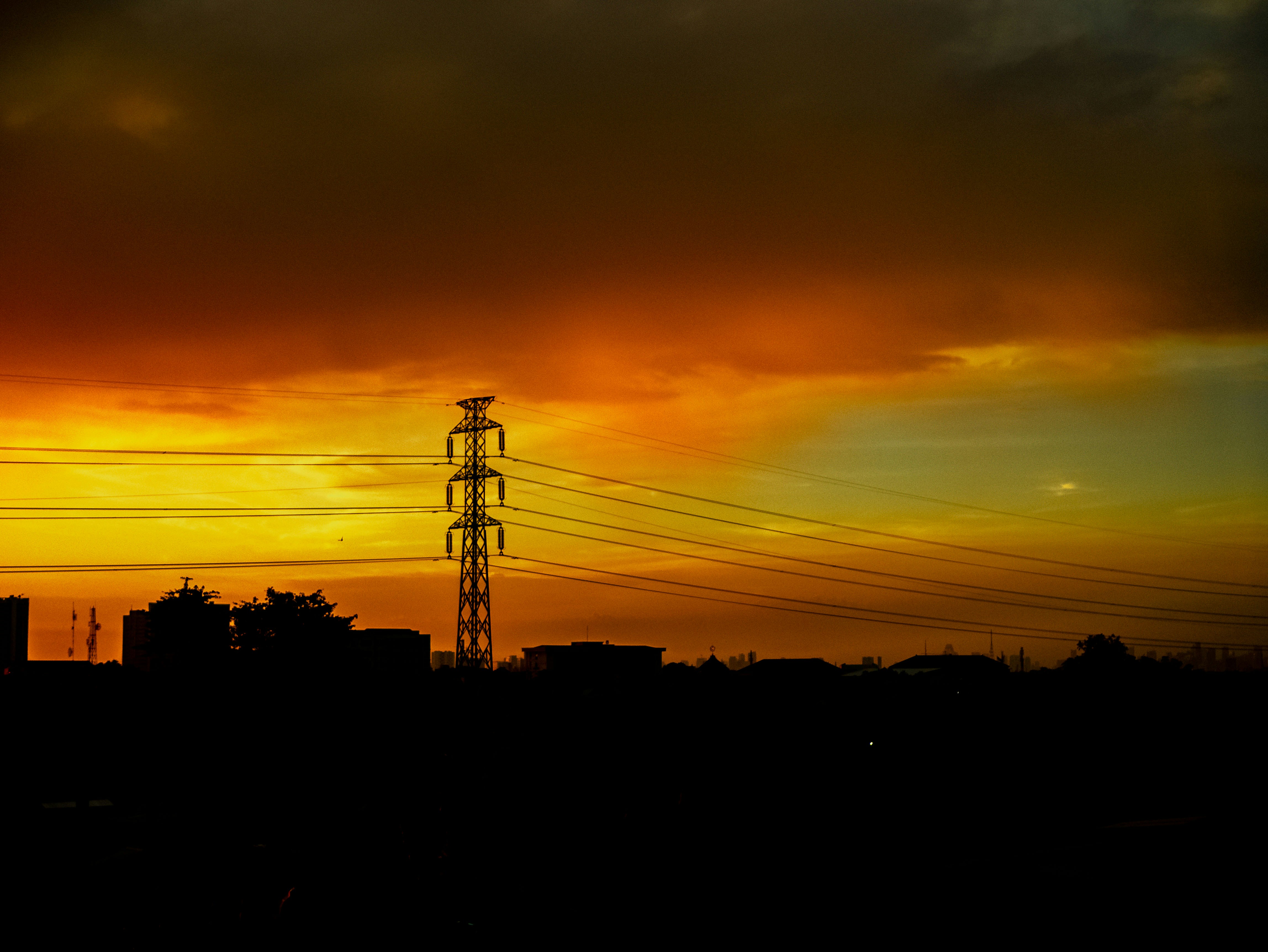 Silhouetted buildings and power lines create a stark contrast against a vibrant sunset sky filled with orange and blue hues.