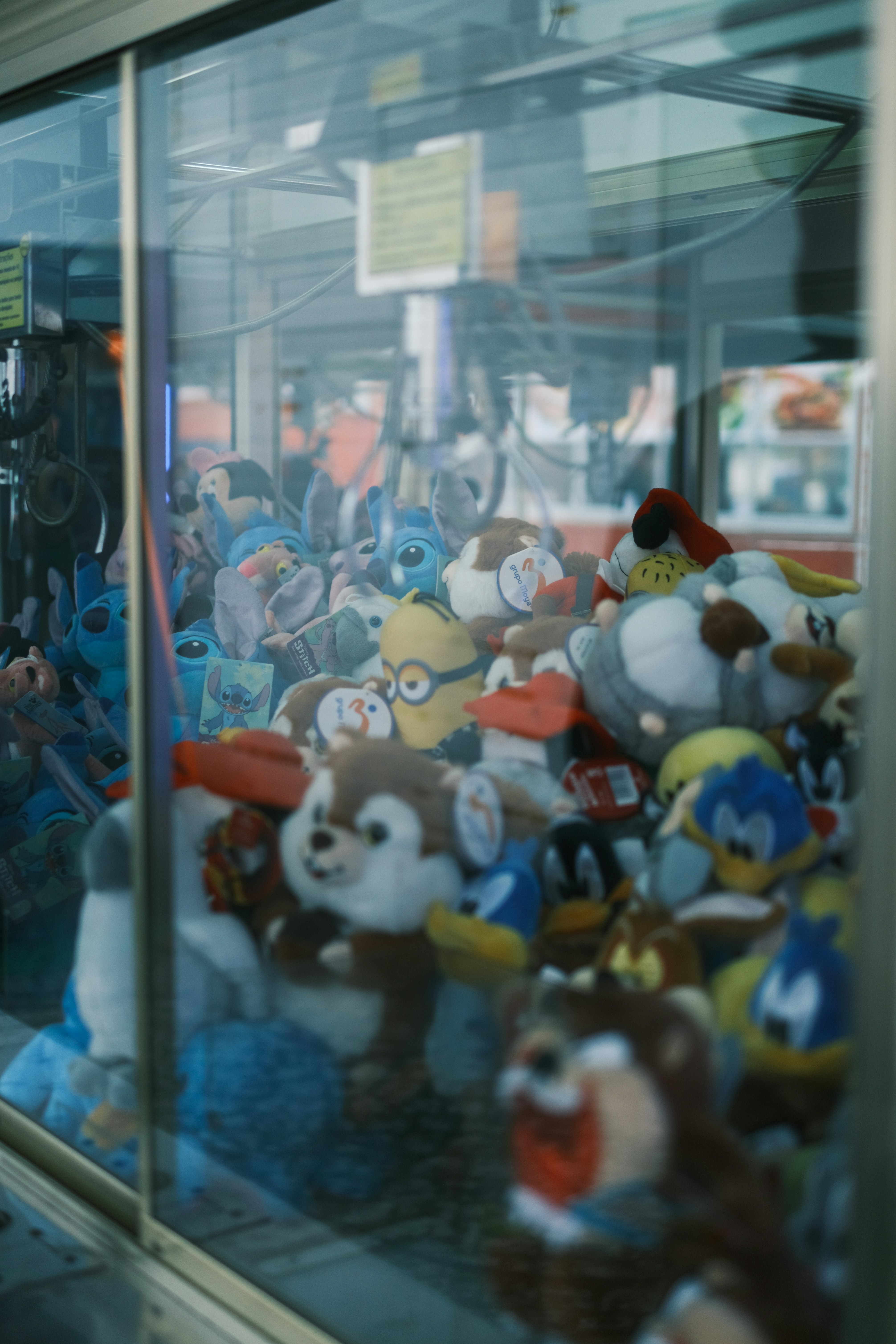 Glass-front claw machine packed with a colorful crowd of plush toys, photographed from outside. The busy prize display hints at a toy-filled arcade moment.