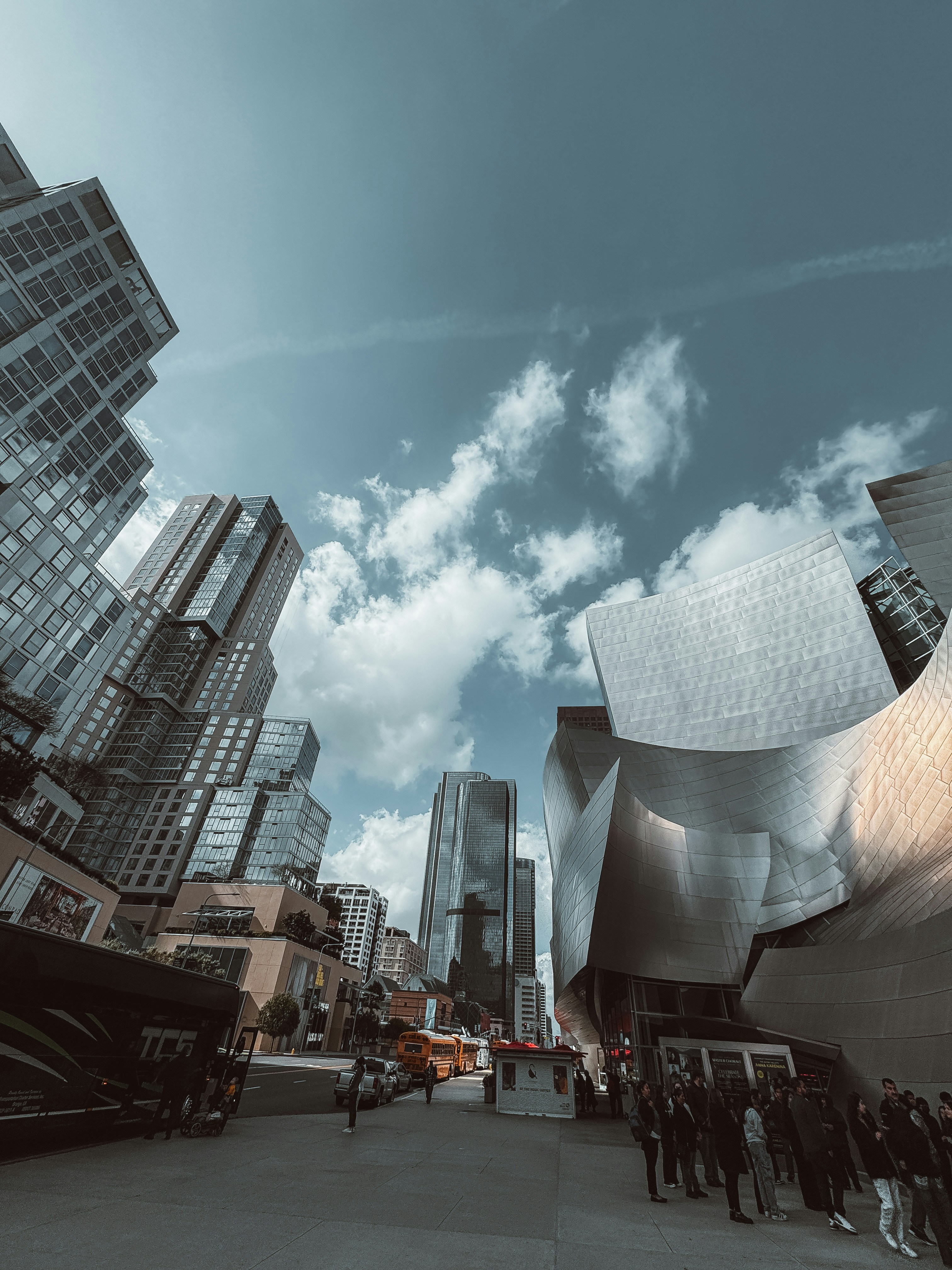 Dynamic cityscape showcasing modern architecture against a vibrant sky, with people gathered in the foreground. The image highlights the interplay of geometric forms and urban life.