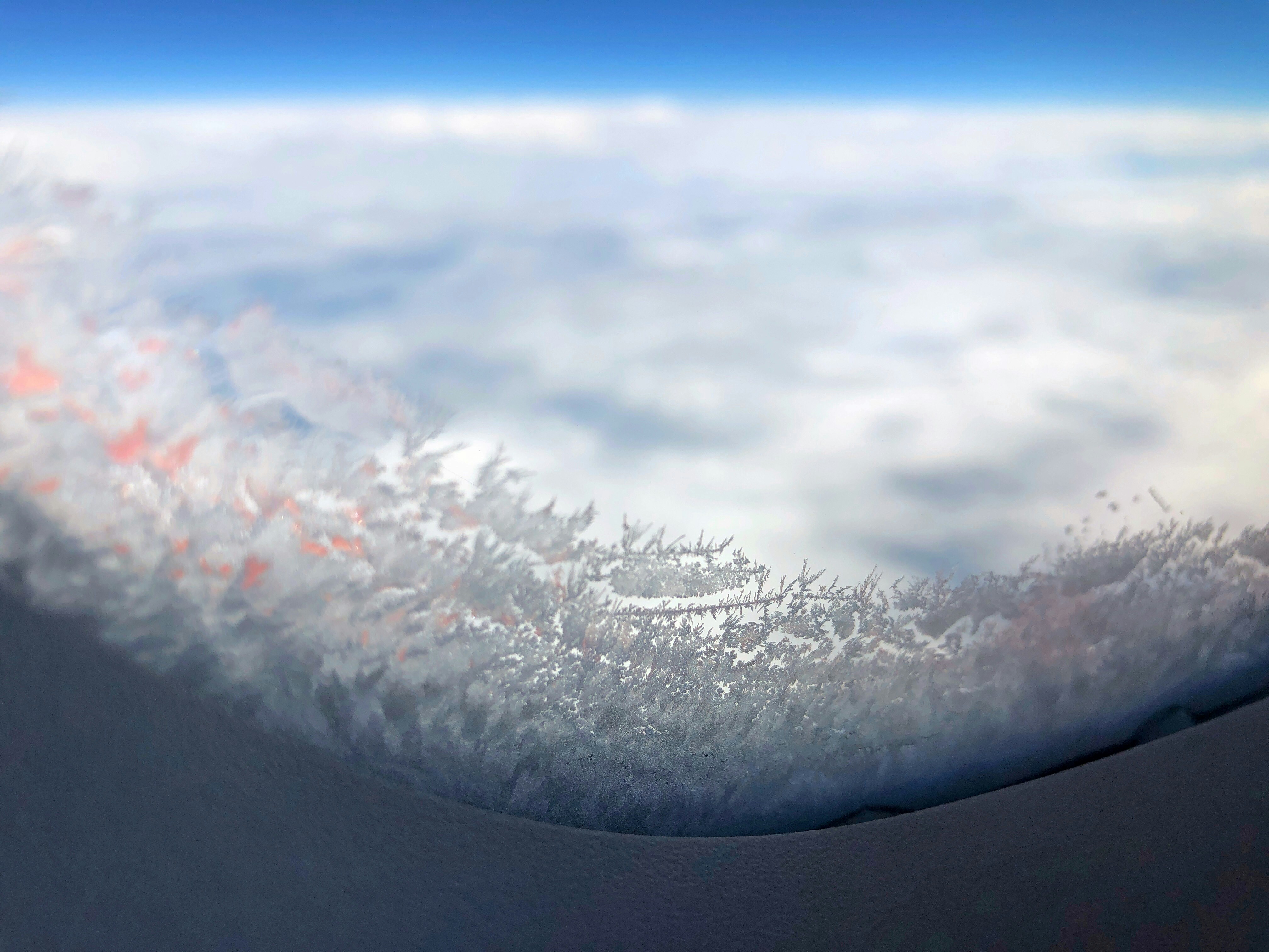 Frosted Window Panorama: Ice Crystals Framing a Sky-Blue Sea of Clouds