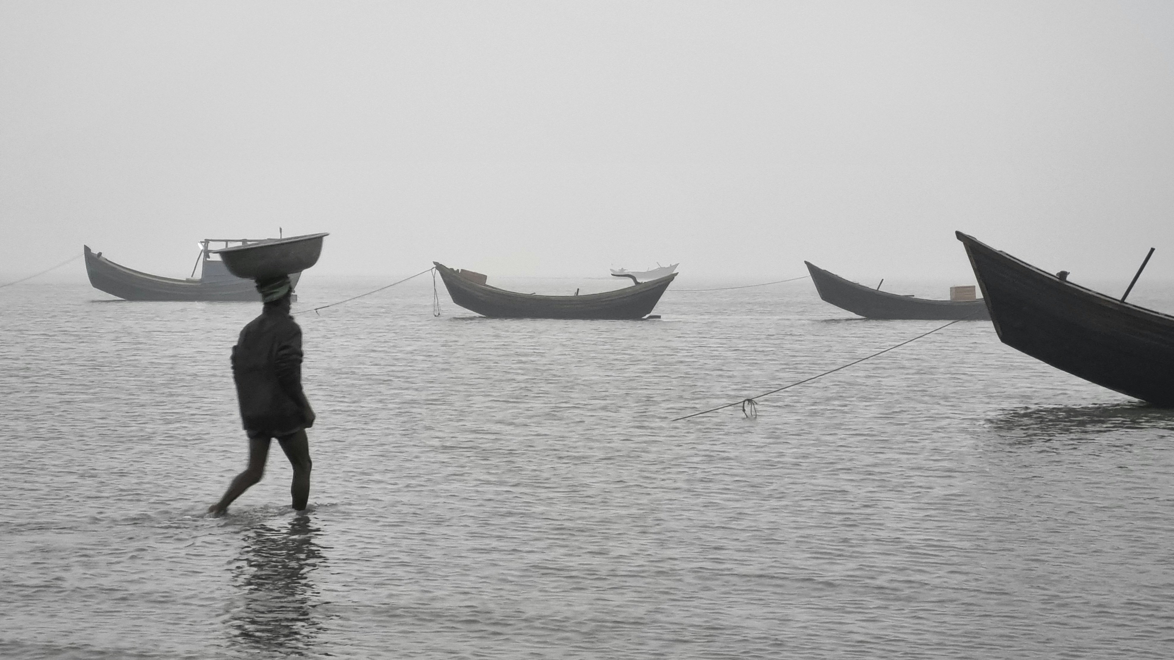 A person walking in the water with three boats in the background photo ...