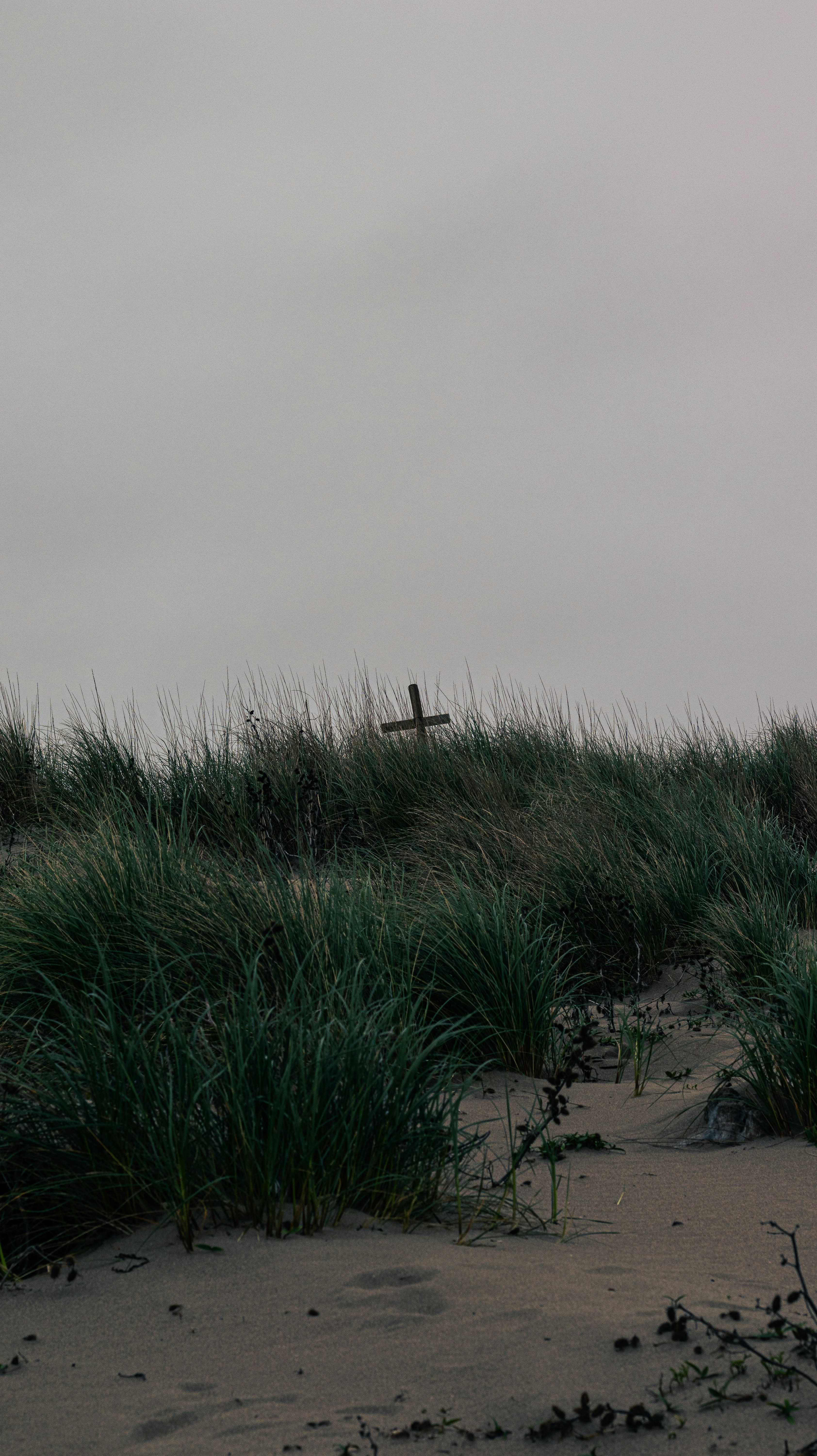 Solitary Cross Above Wind-Swept Dunes Under a Gray Coastal Sky