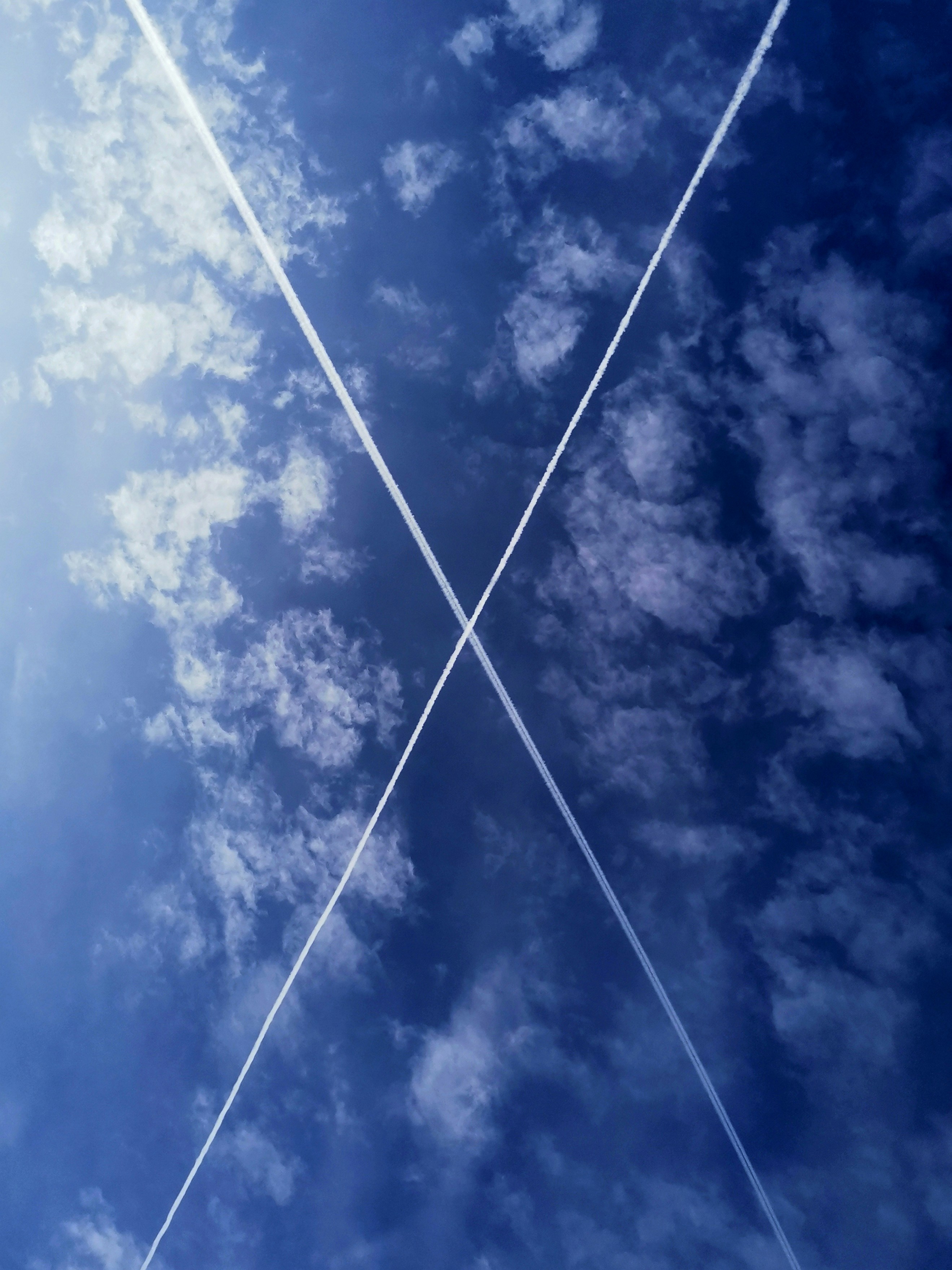 Blue sky with wispy clouds intersected by two white contrails forming an X across the frame.