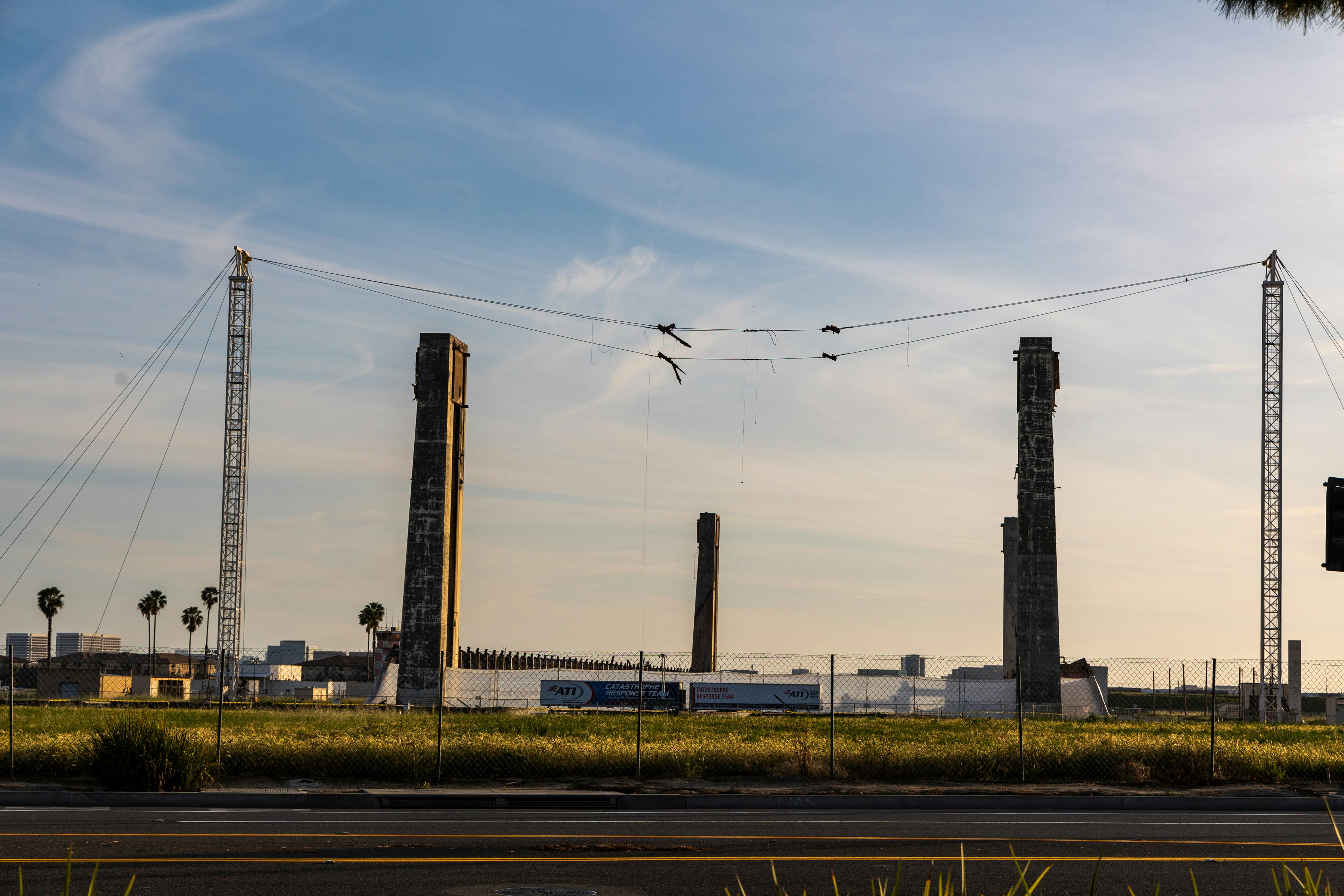 Abandoned industrial towers stand against a golden sky, framed by construction cranes, evoking a sense of nostalgia and transformation.