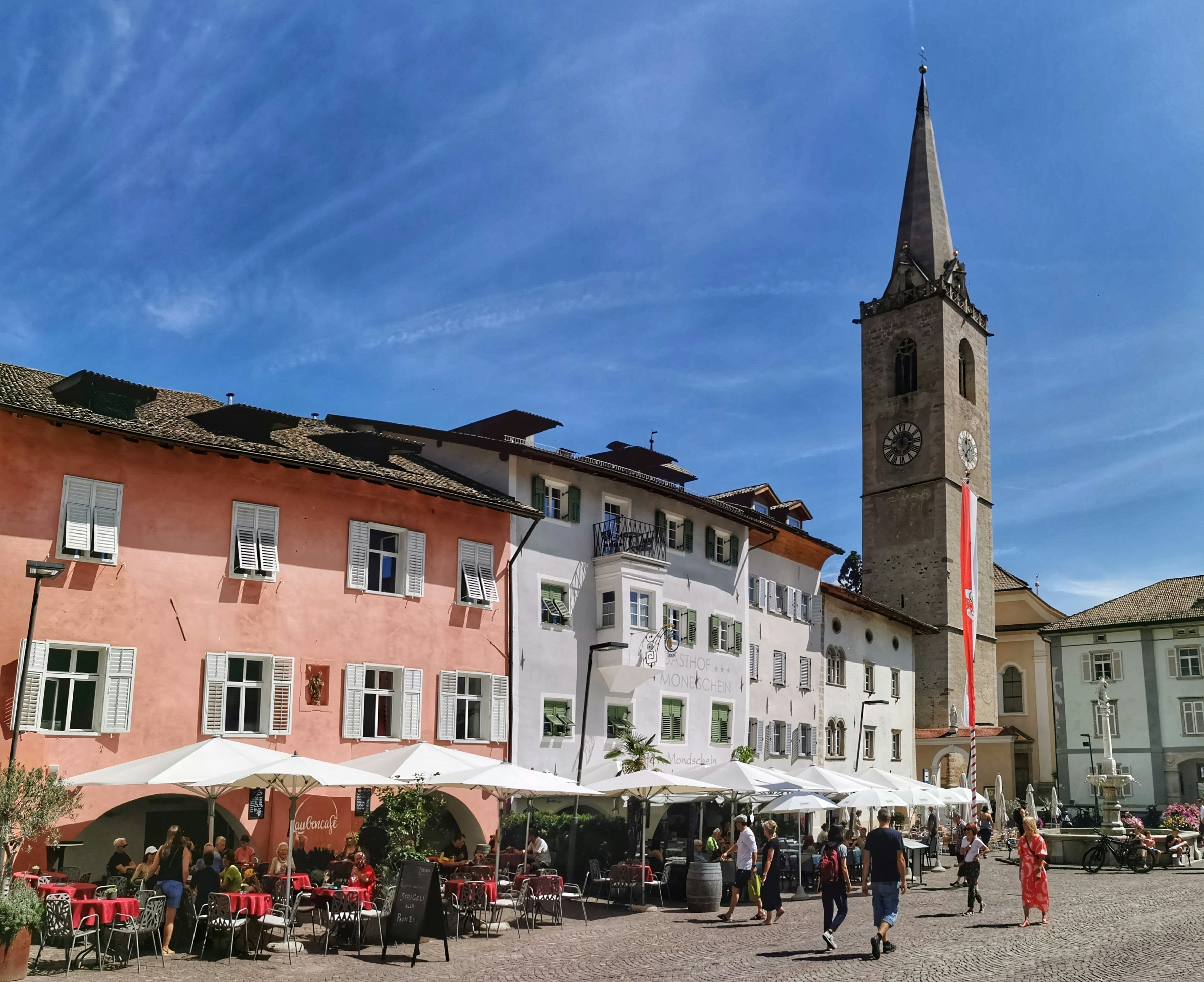 Colorful buildings and a church tower under a blue sky in a lively town square.