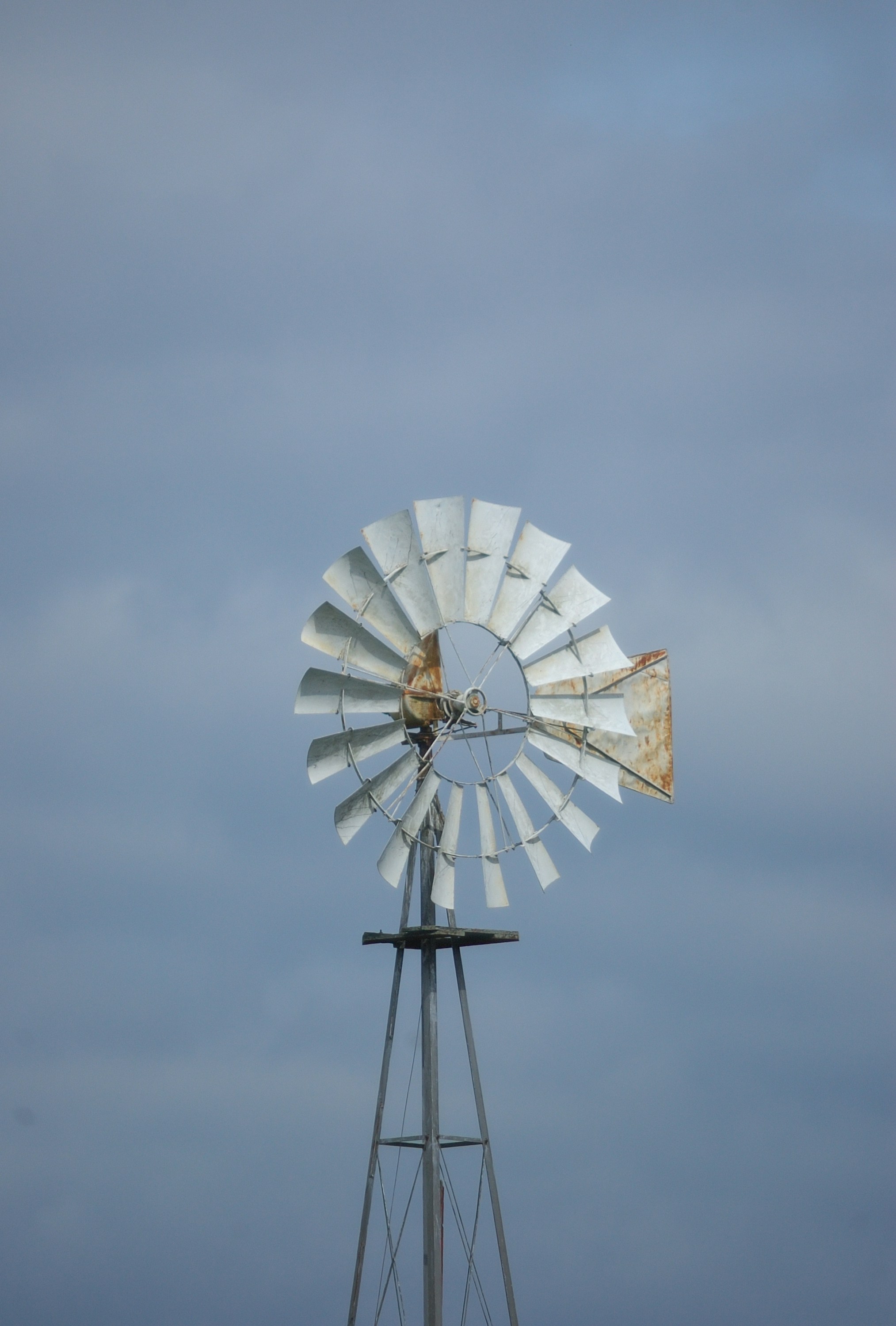 Hub and Halo: Rusted Windmill Wheel Against a Cloudy Blue Sky