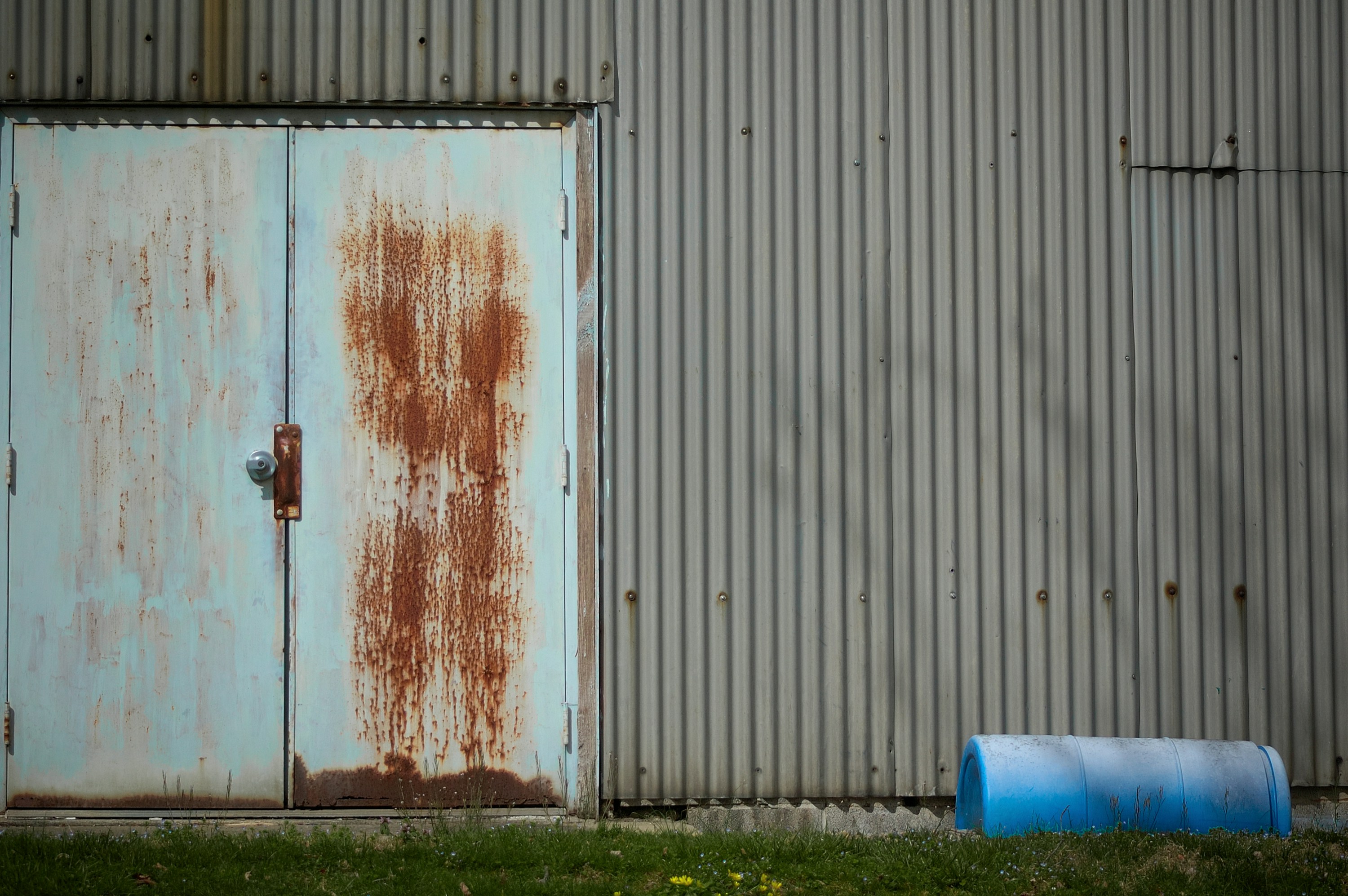 Rust-streaked Turquoise Door Anchored by a Ribbed Steel Wall
