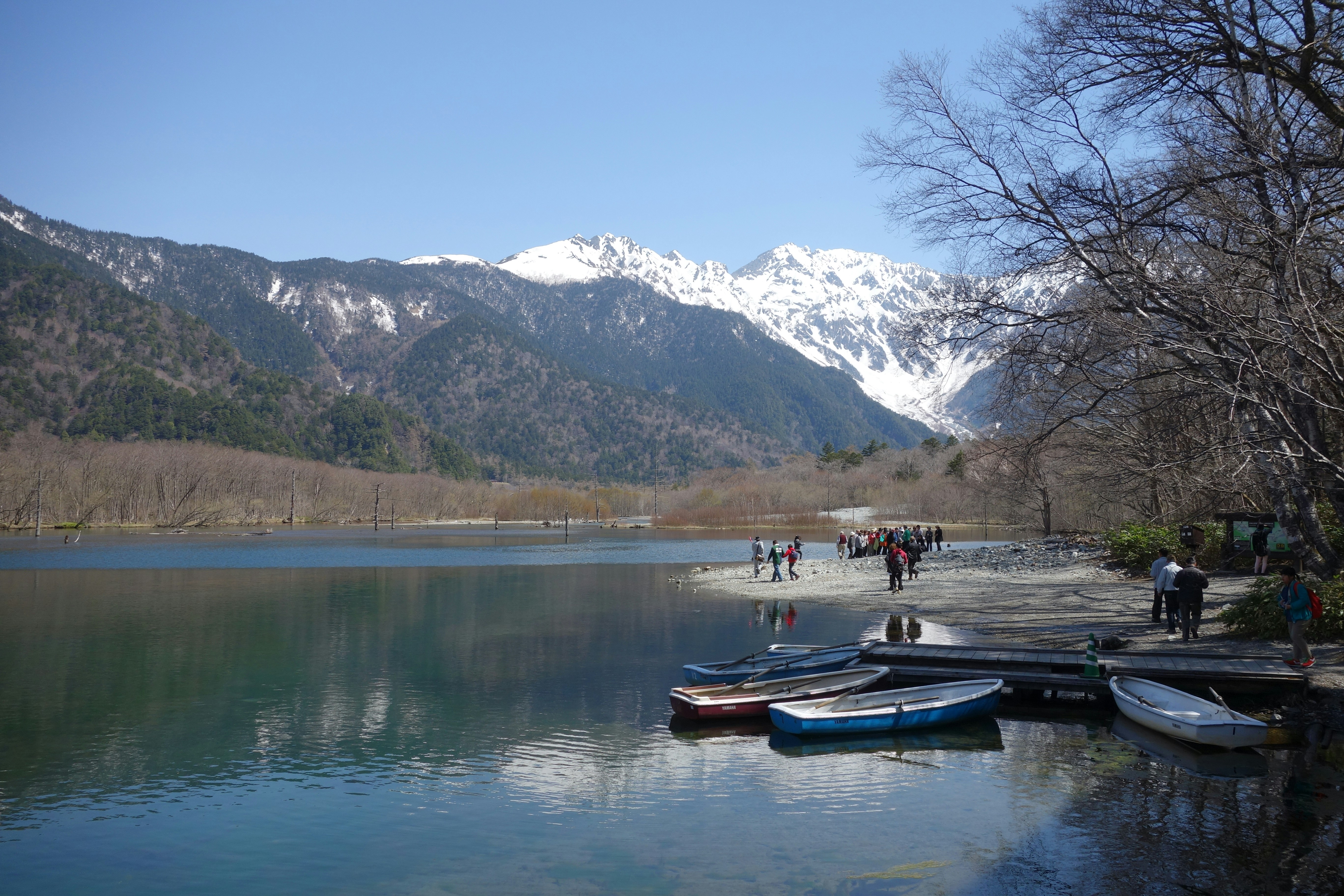 Rowboats lined along the shore of a tranquil lake, with snow-capped mountains in the background and visitors enjoying the scenic beauty.
