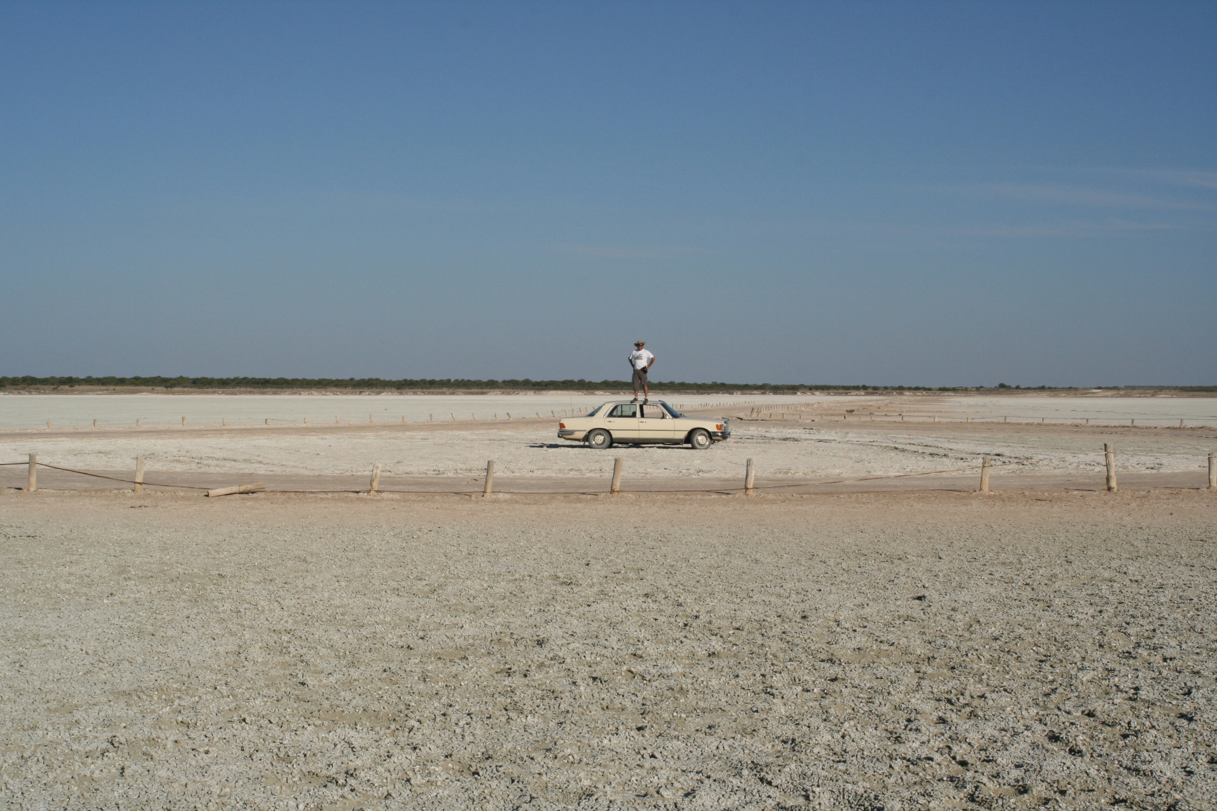 Standby on the Salt Plain: A Lone Figure Surfs the Horizon in a Vintage Car