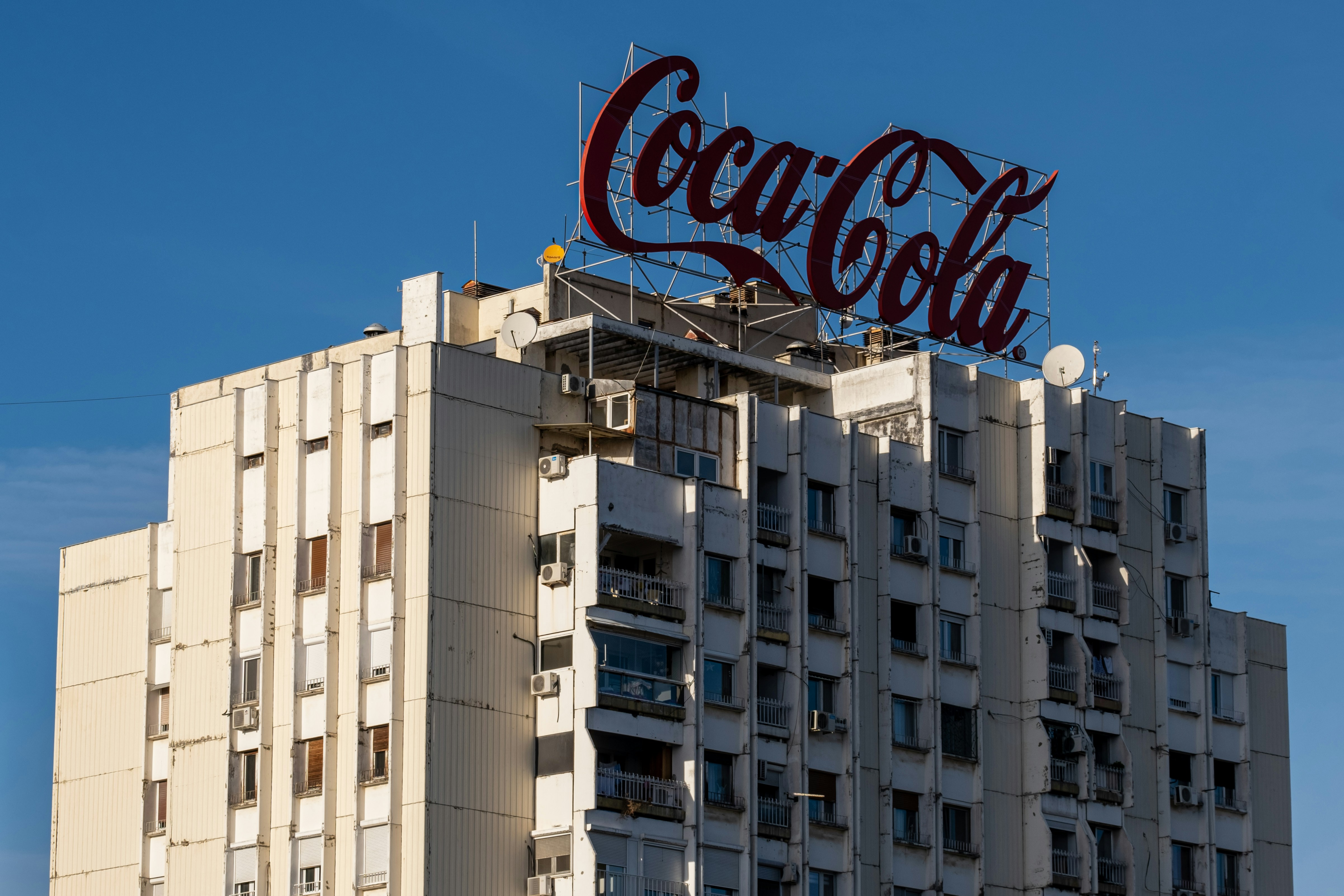Large Coca-Cola sign atop a tall building against a clear blue sky.