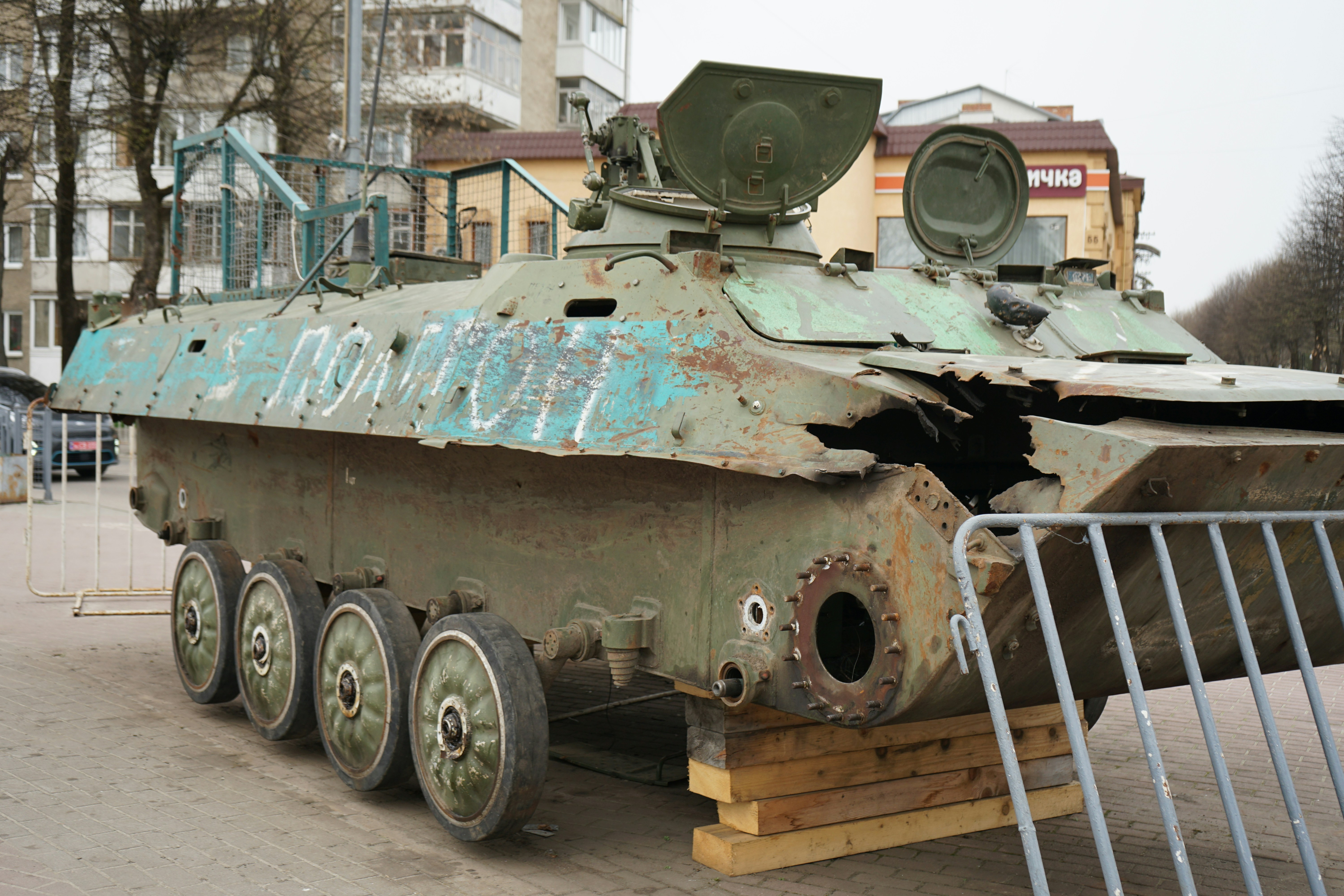 Weathered armored hull on a city street guarded by metal barriers