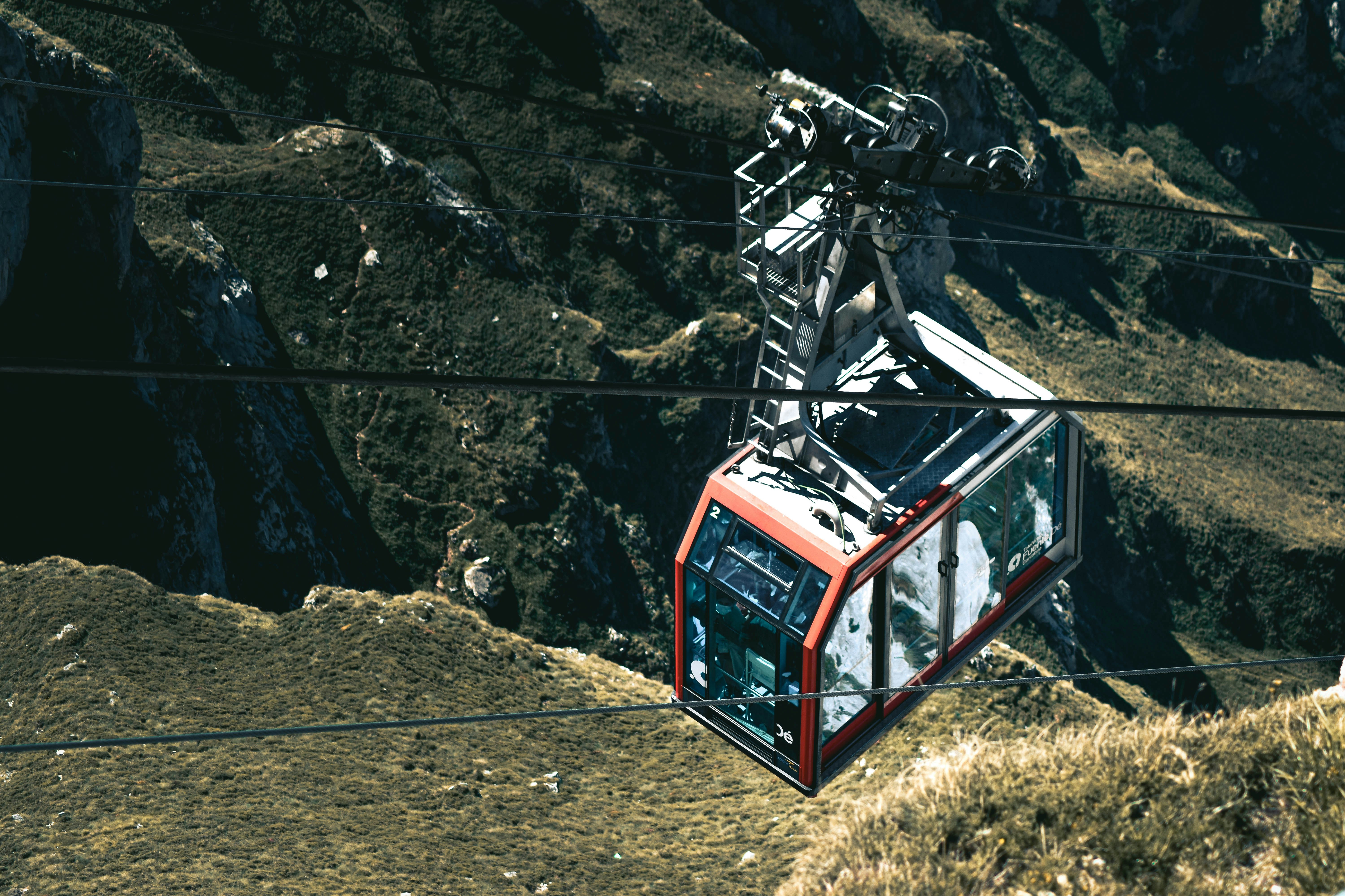 Red cable car suspended over rugged mountain terrain.