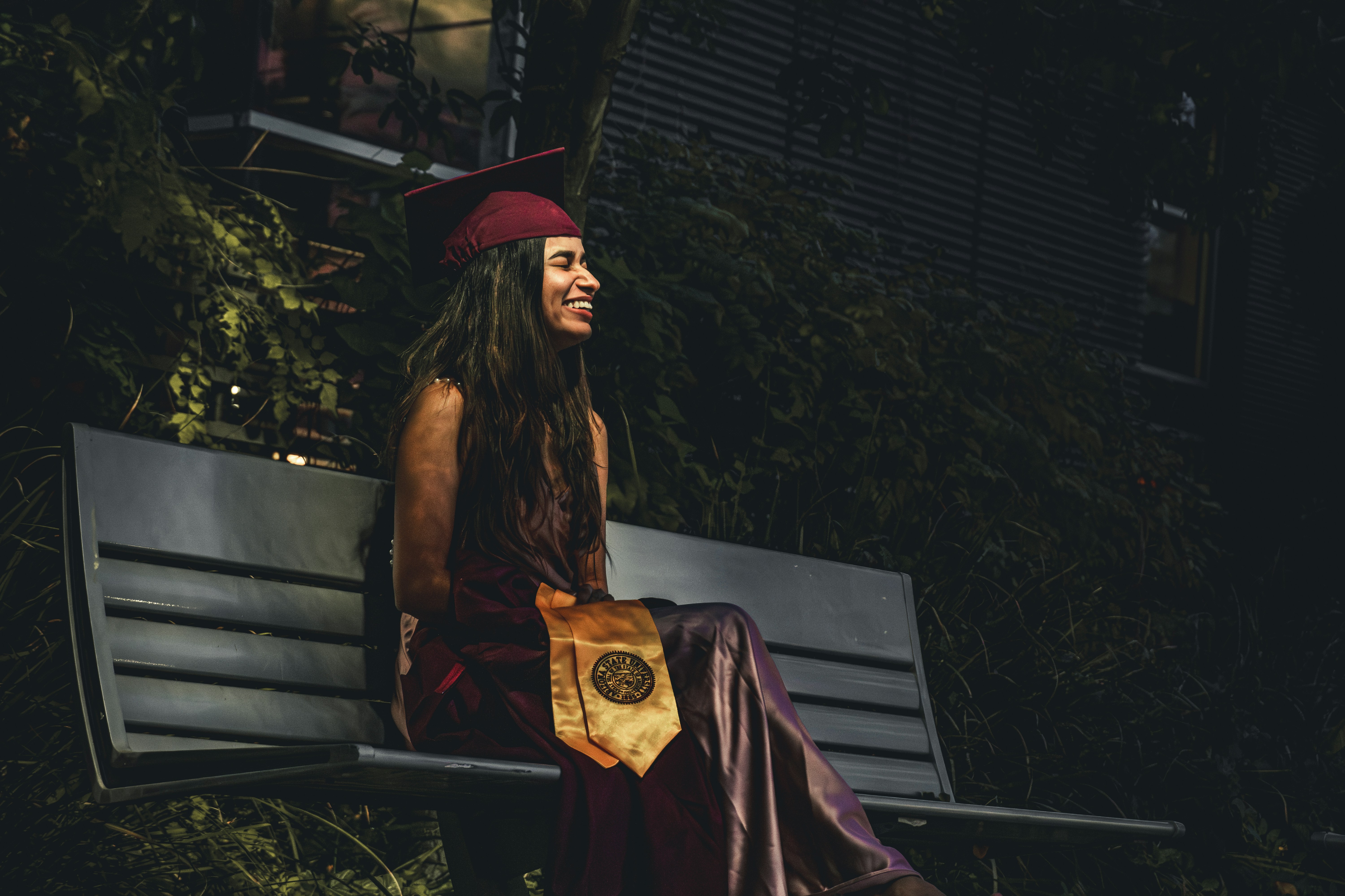 A woman in a graduation gown sitting on a bench photo – Free Woman ...