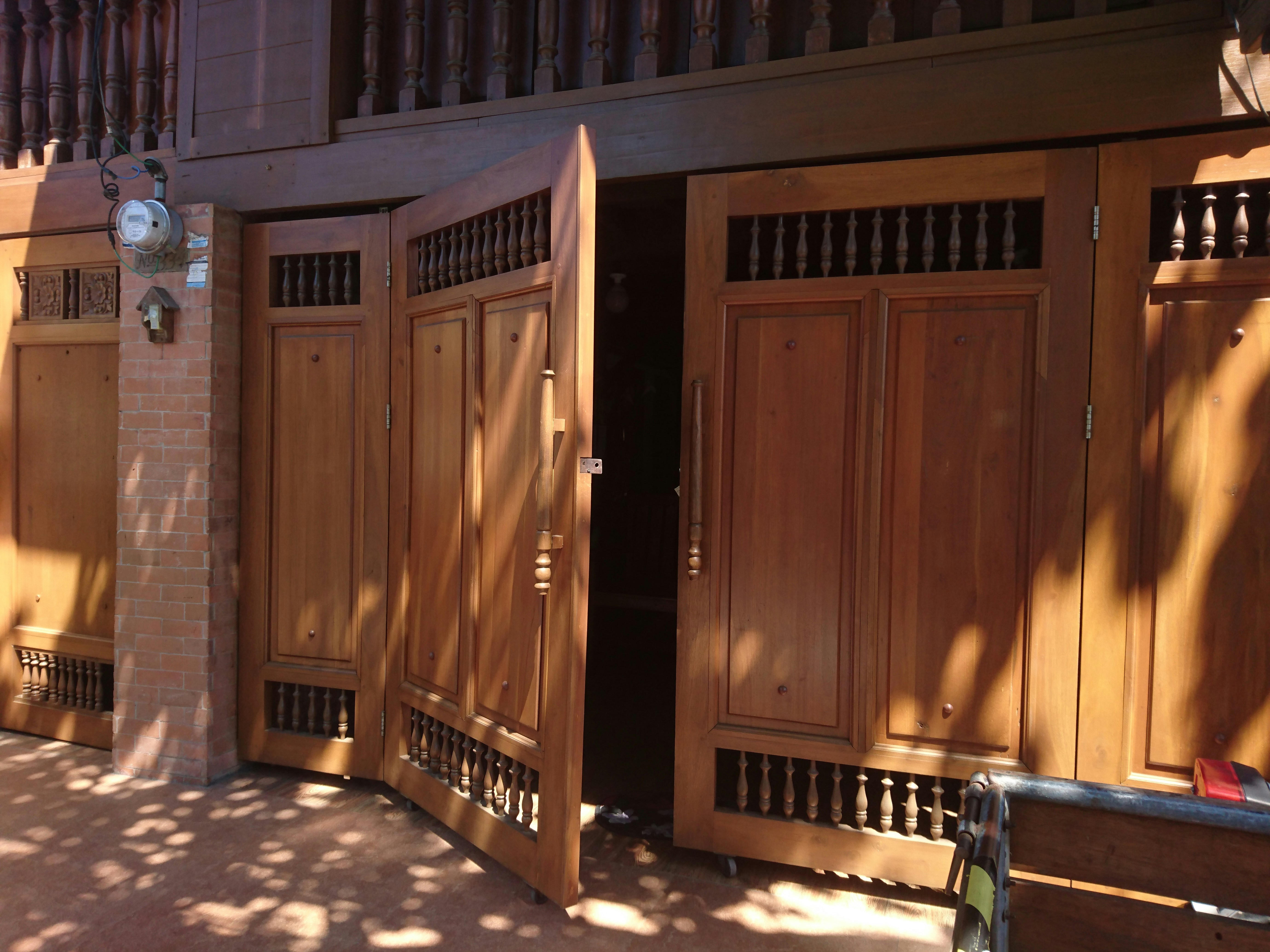 Photograph captures warm afternoon light spilling across carved wooden doors with open panels revealing a dark interior.