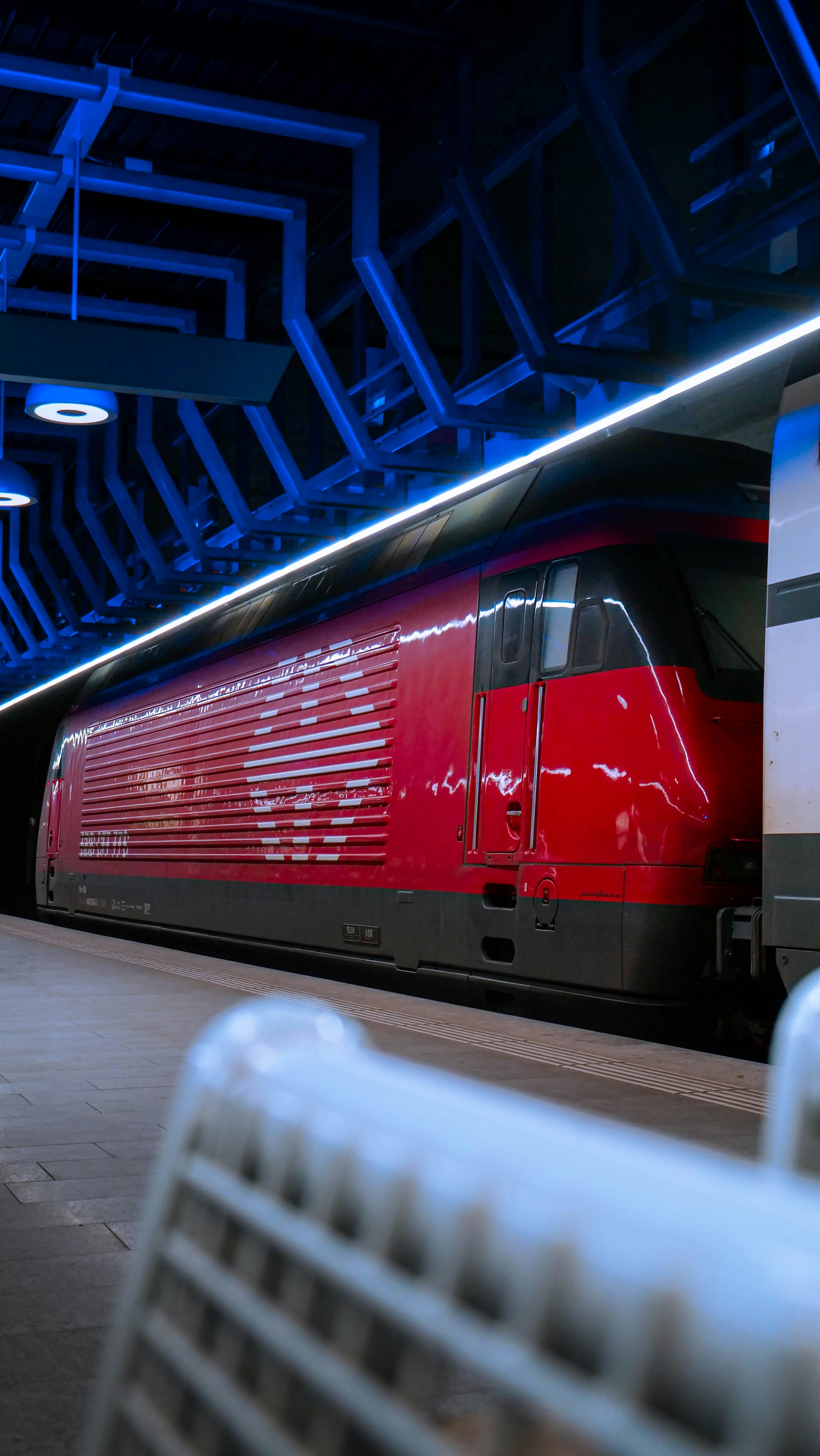 Red locomotive on a platform beneath neon-blue girders, captured in a moody underground scene.