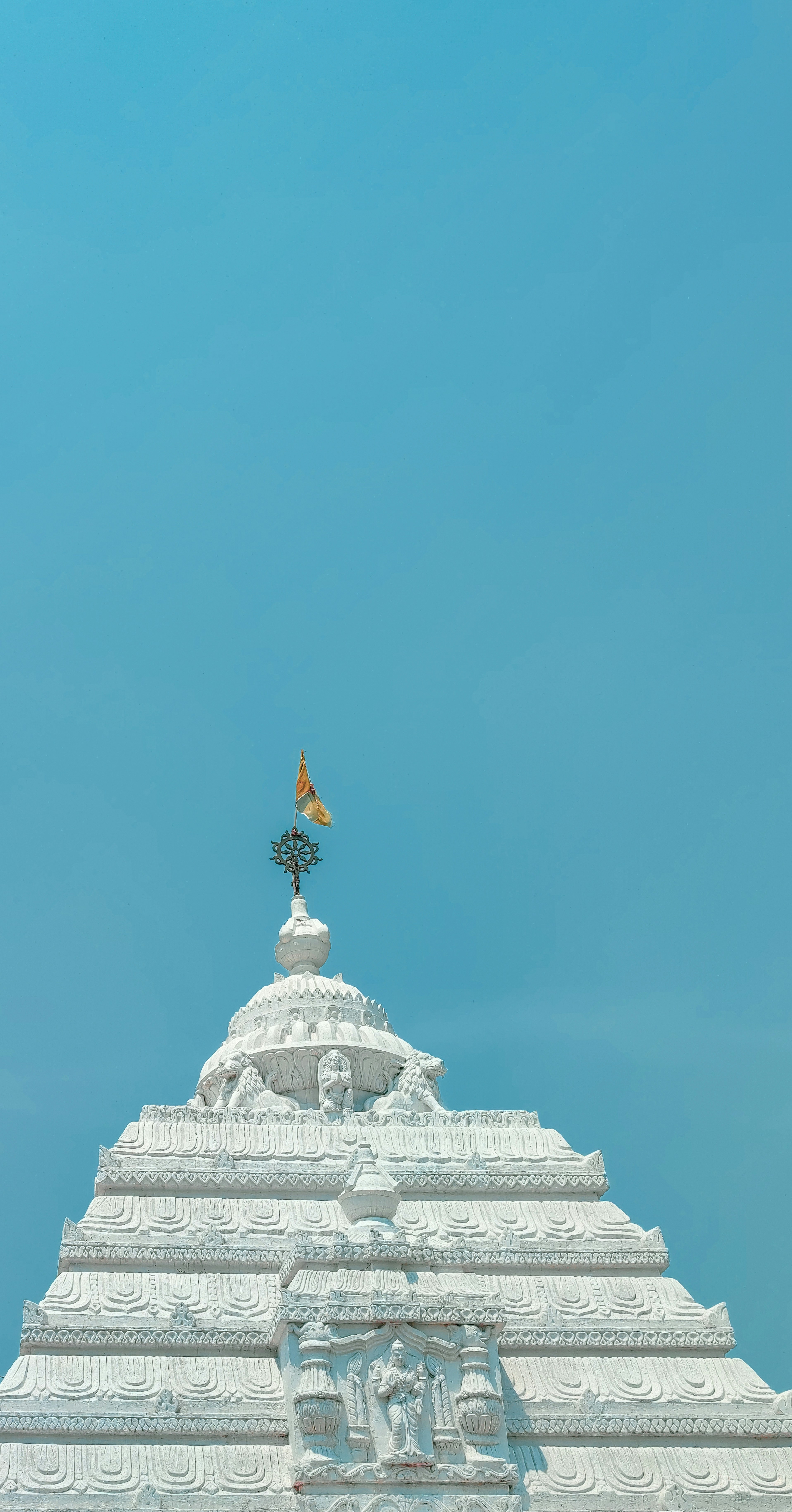 White tiered temple spire rises against a clear blue sky, crowned with a flag.