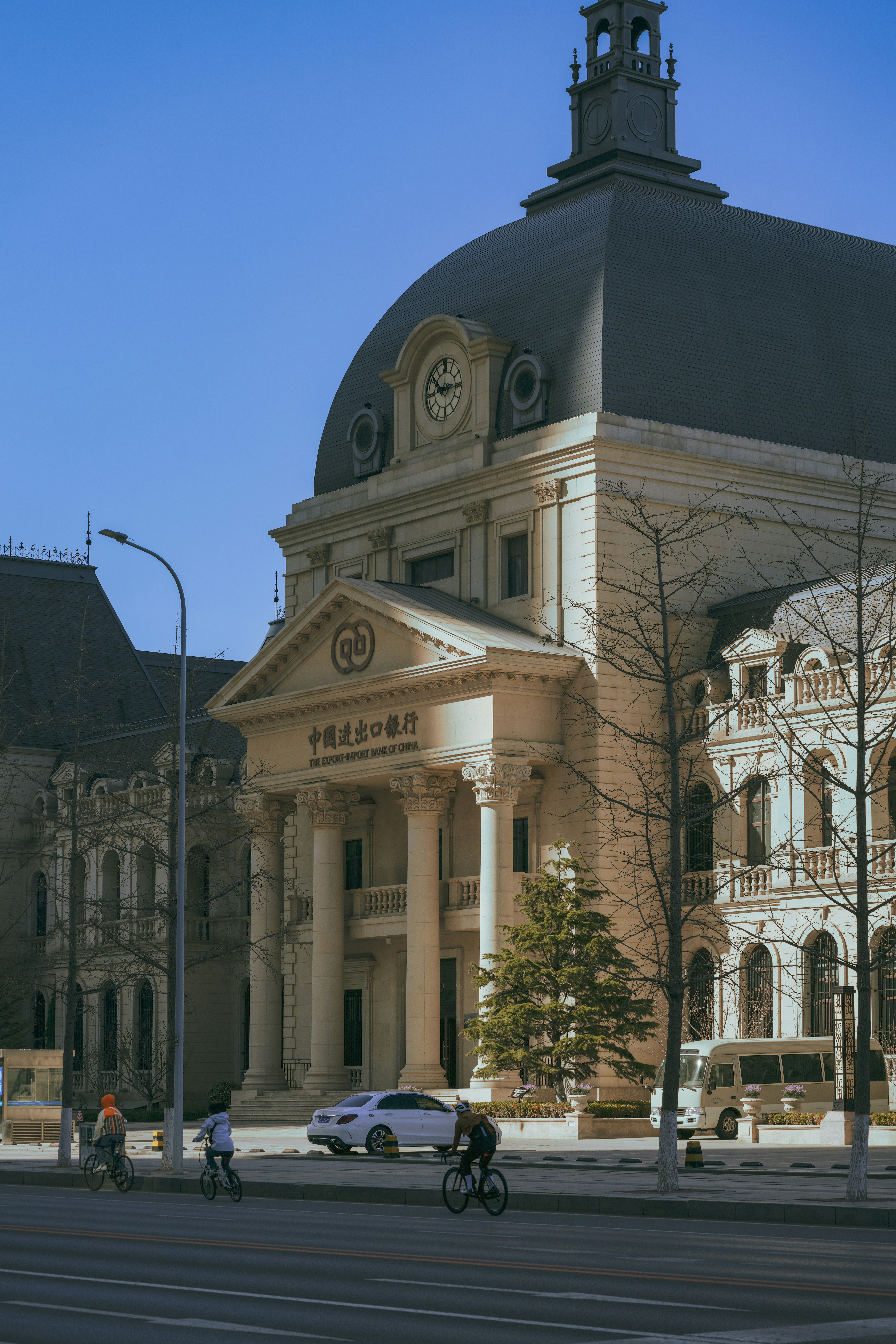Historic building featuring classical architecture, complemented by cyclists passing by on a sunny day.