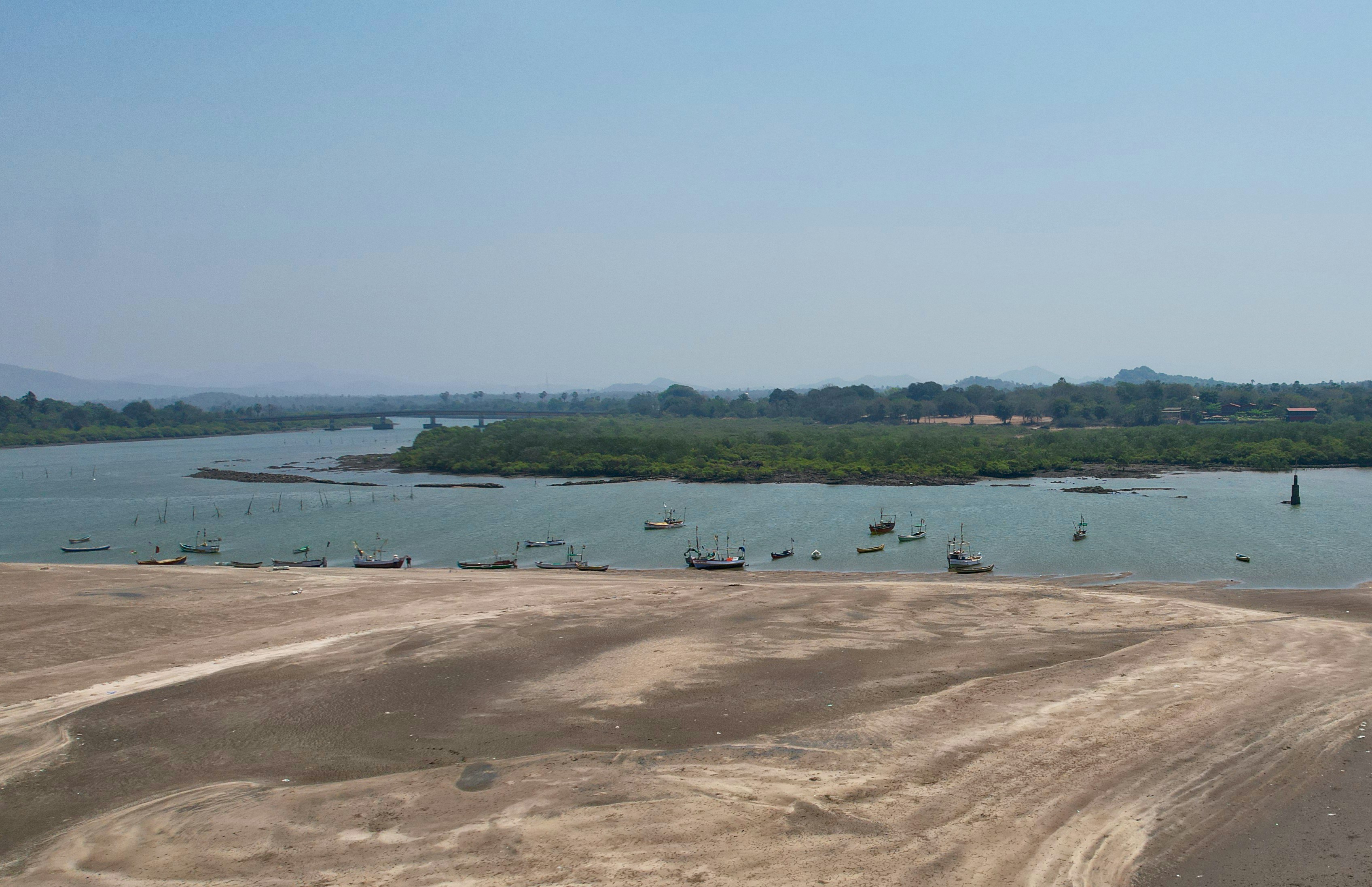 Tranquil river scene with fishing boats scattered across the water, surrounded by lush greenery and distant hills.
