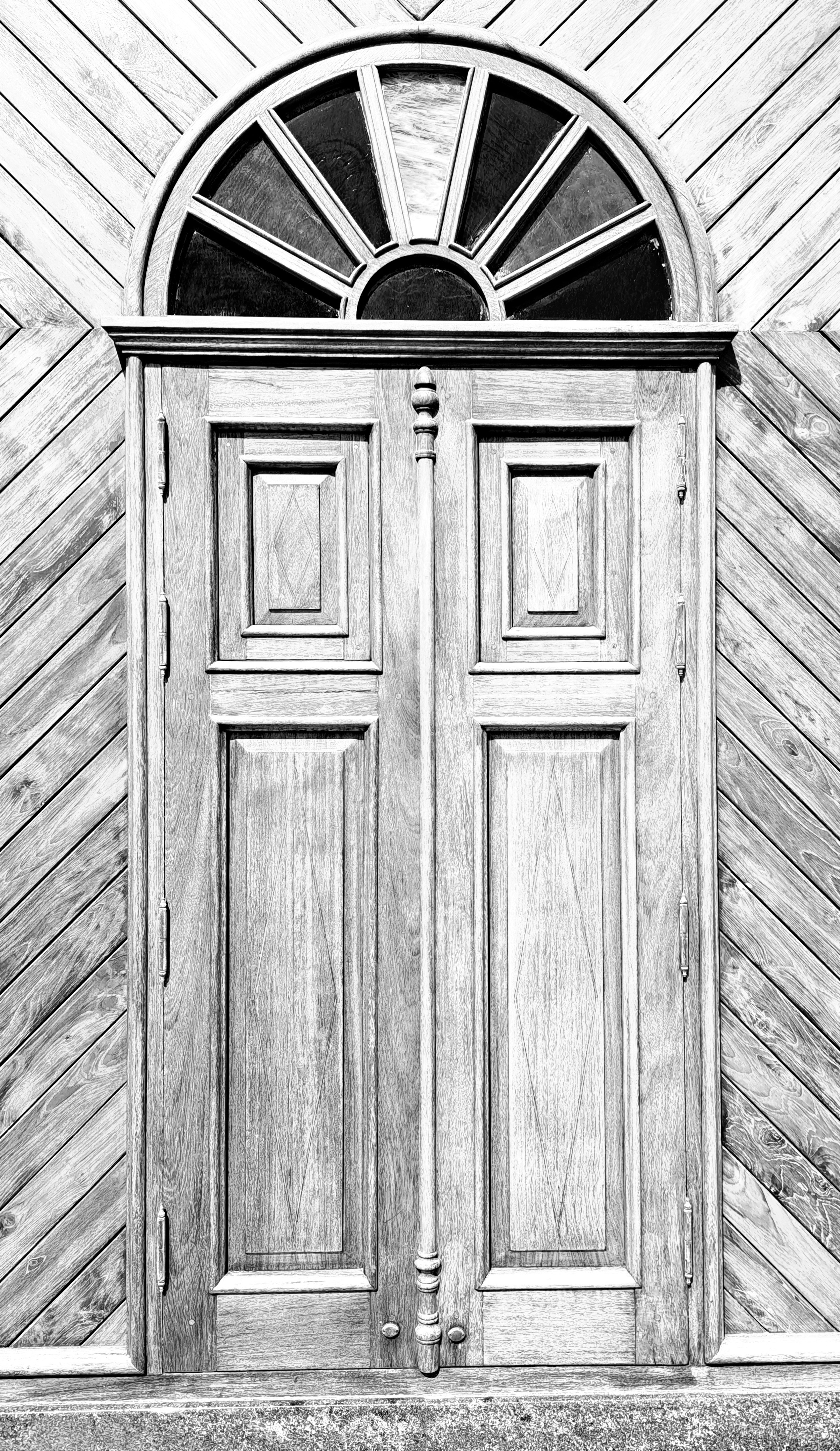 Threshold in Monochrome: Weathered Door Framed by Chevron Siding and a Semi-Circular Transom