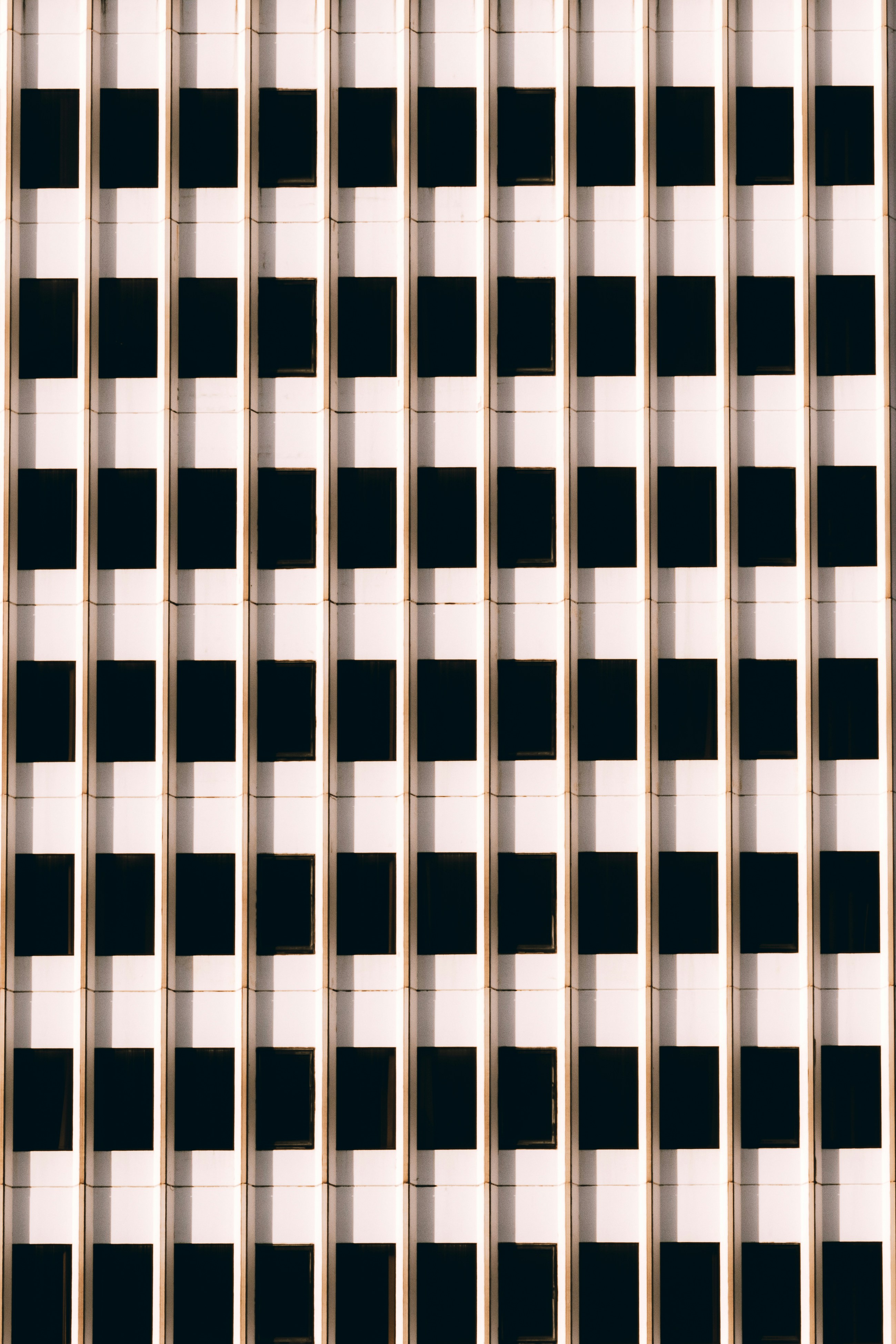 A symmetrical arrangement of windows on a modern building, showcasing a pattern of light and shadow. The design emphasizes architectural lines and shapes.