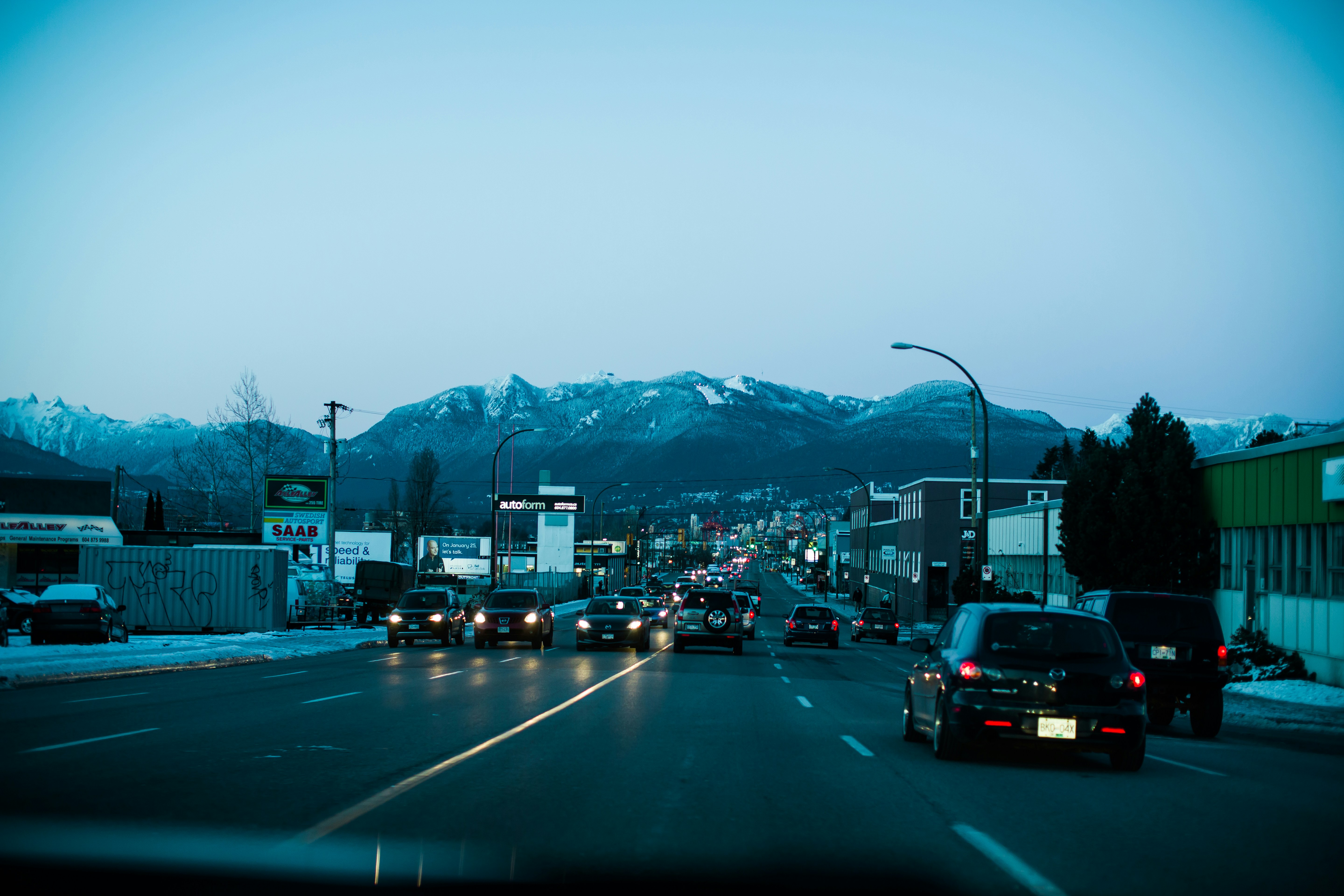 Busy street scene with vehicles traveling towards distant mountains at twilight, showcasing a blend of urban and natural elements.