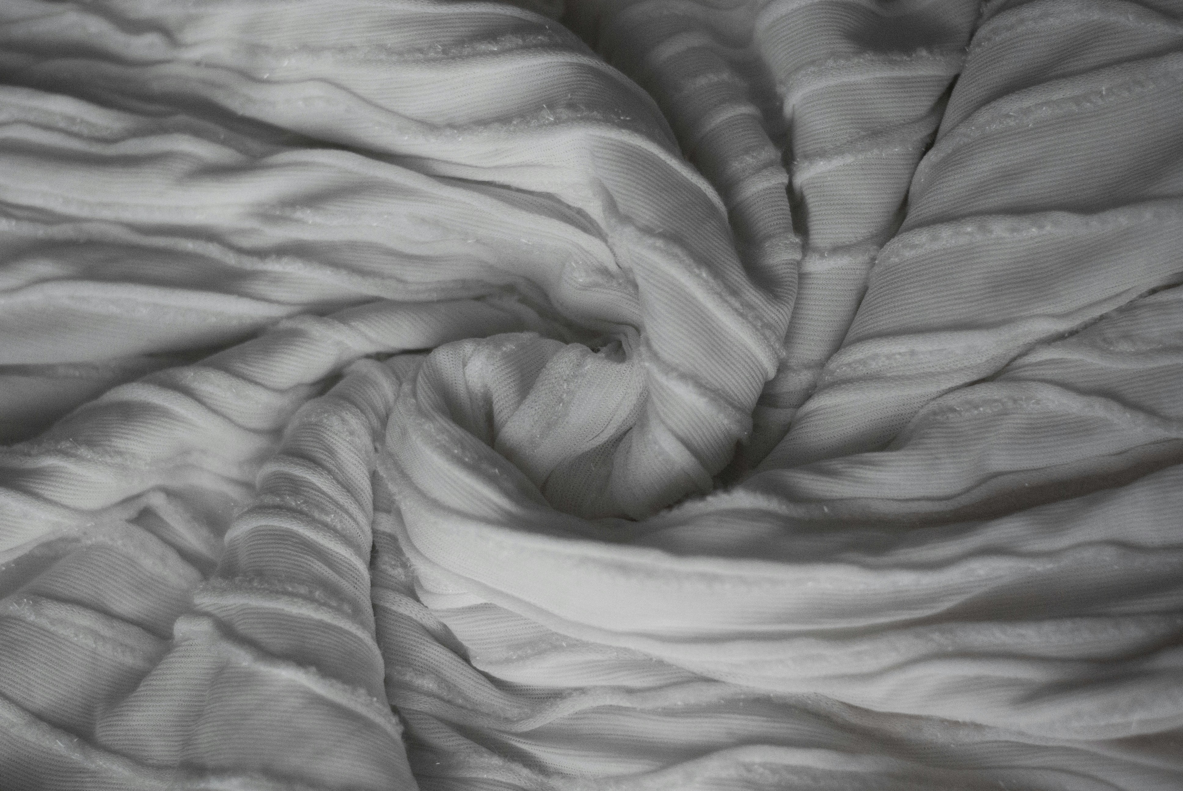 Close-up of intricately folded white fabric, showcasing its texture and subtle patterns. The gentle curves create a sense of movement.