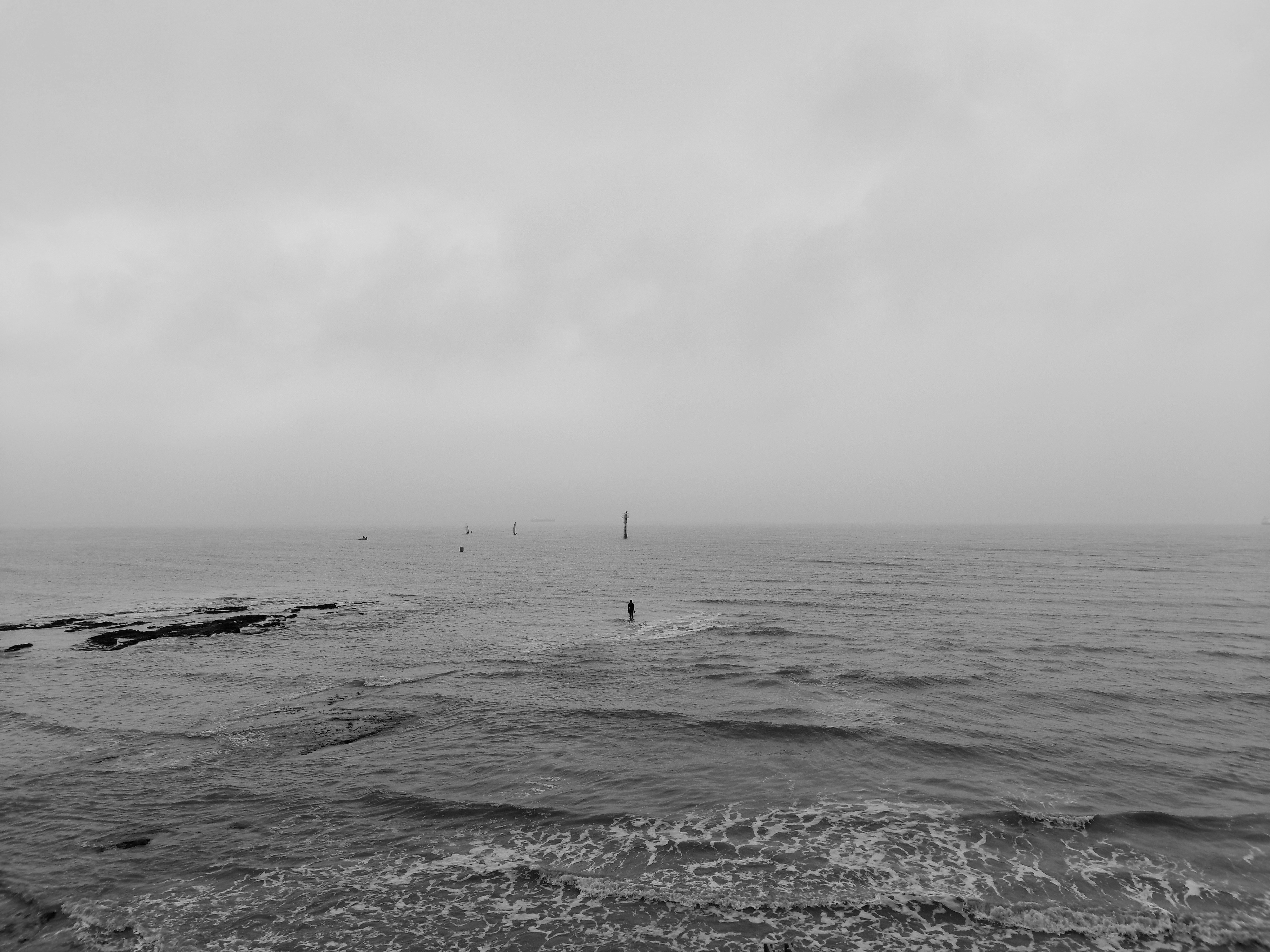 Solitary figure navigating the vast ocean under a cloudy sky.